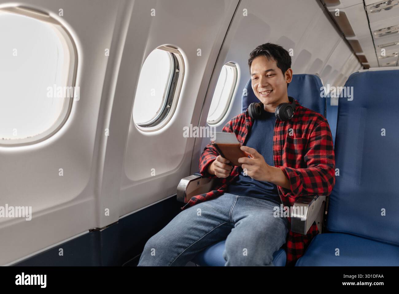 A young man sits on a window seat inside an airplane, holding his ...
