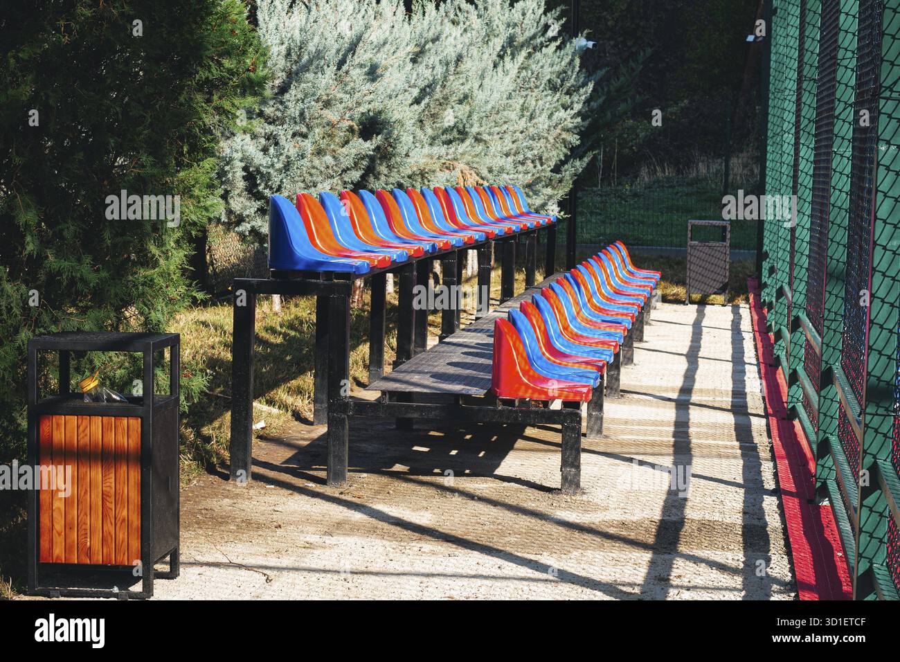Brightly colored benches line a path beside a sports field in a park ...