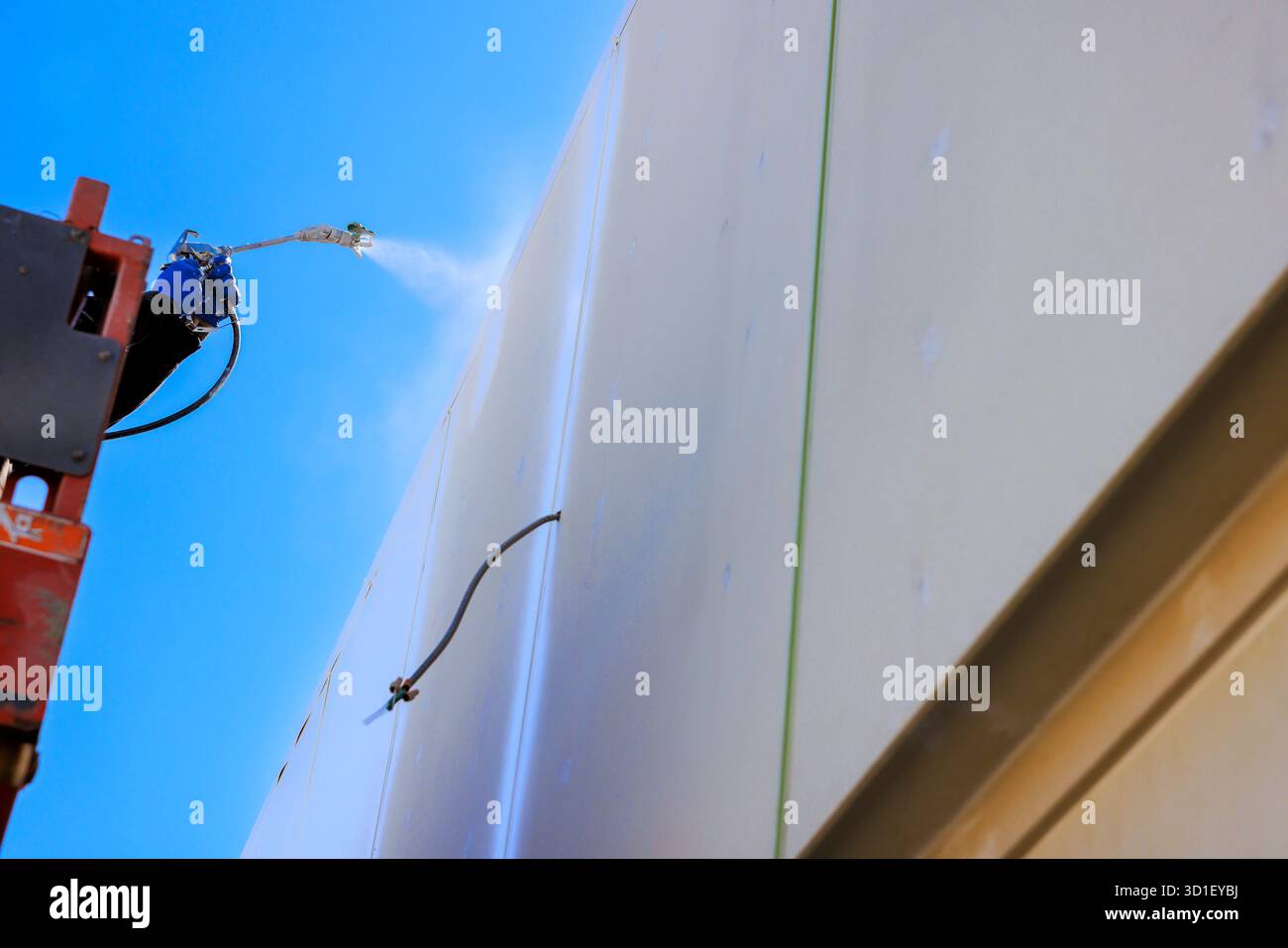 Worker uses spray tool apply paint on building wall while elevated on ...
