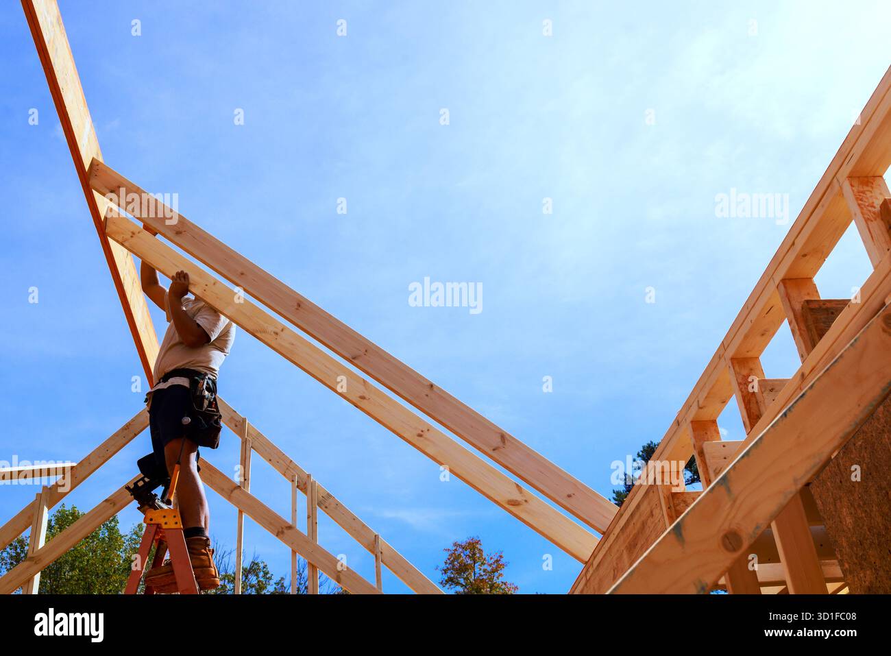Worker on ladder installs rafters roof beams on new house assembly ...