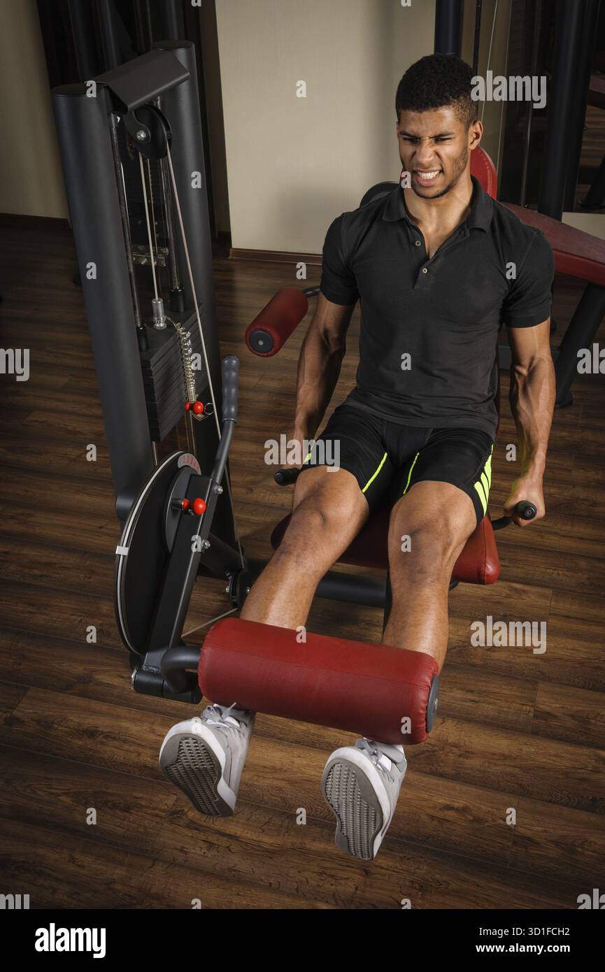 Handsome young african descent Mixed-race man doing legs extensions ...