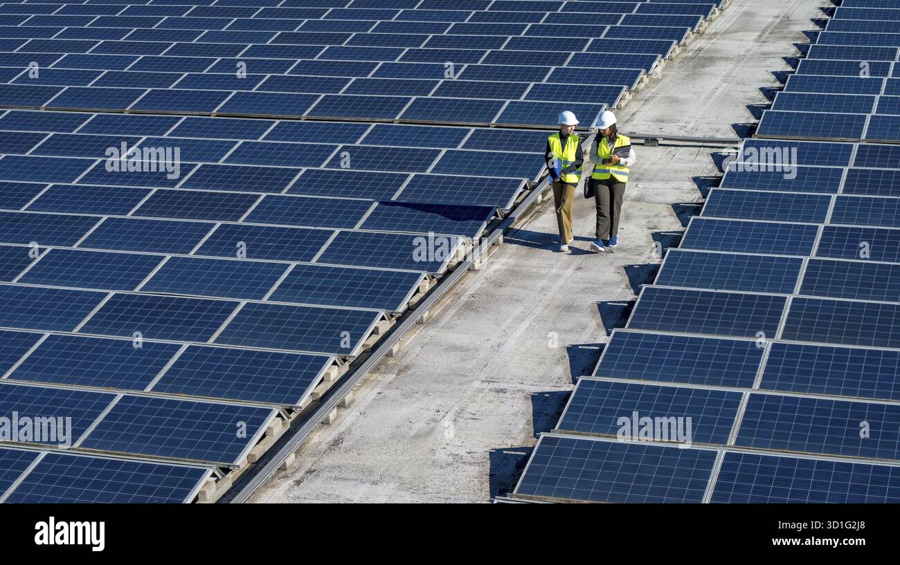 Two engineers wearing hard hats and safety vests walking on a rooftop ...