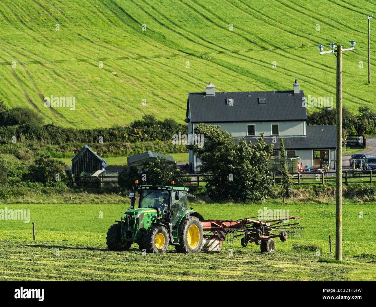 West Cork, Ireland, August 25, 2023. A green tractor with a hay rake is ...