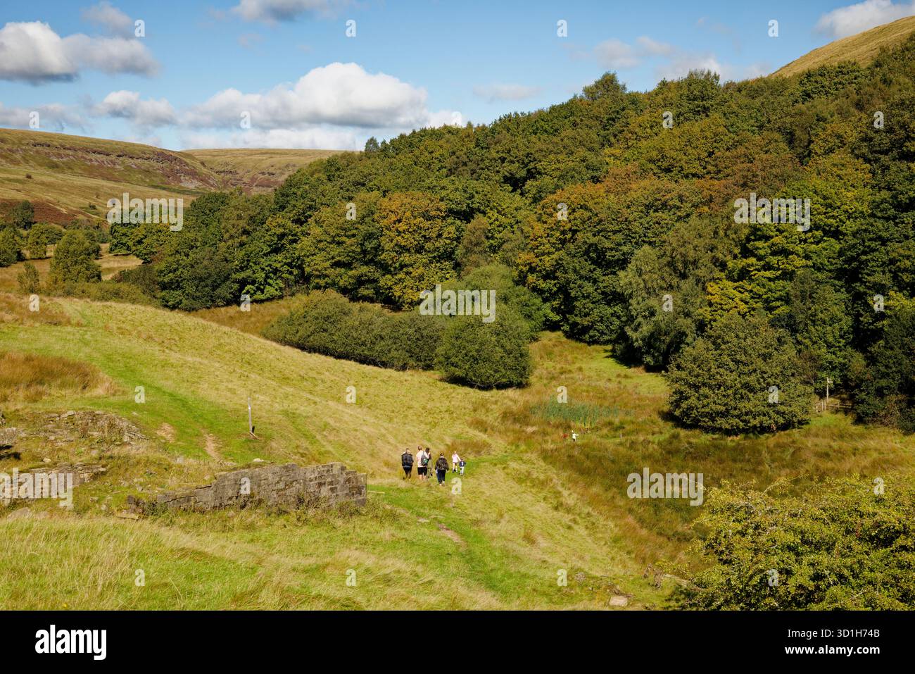 A family group walk down a path in a hilly landscape with woodland and ...