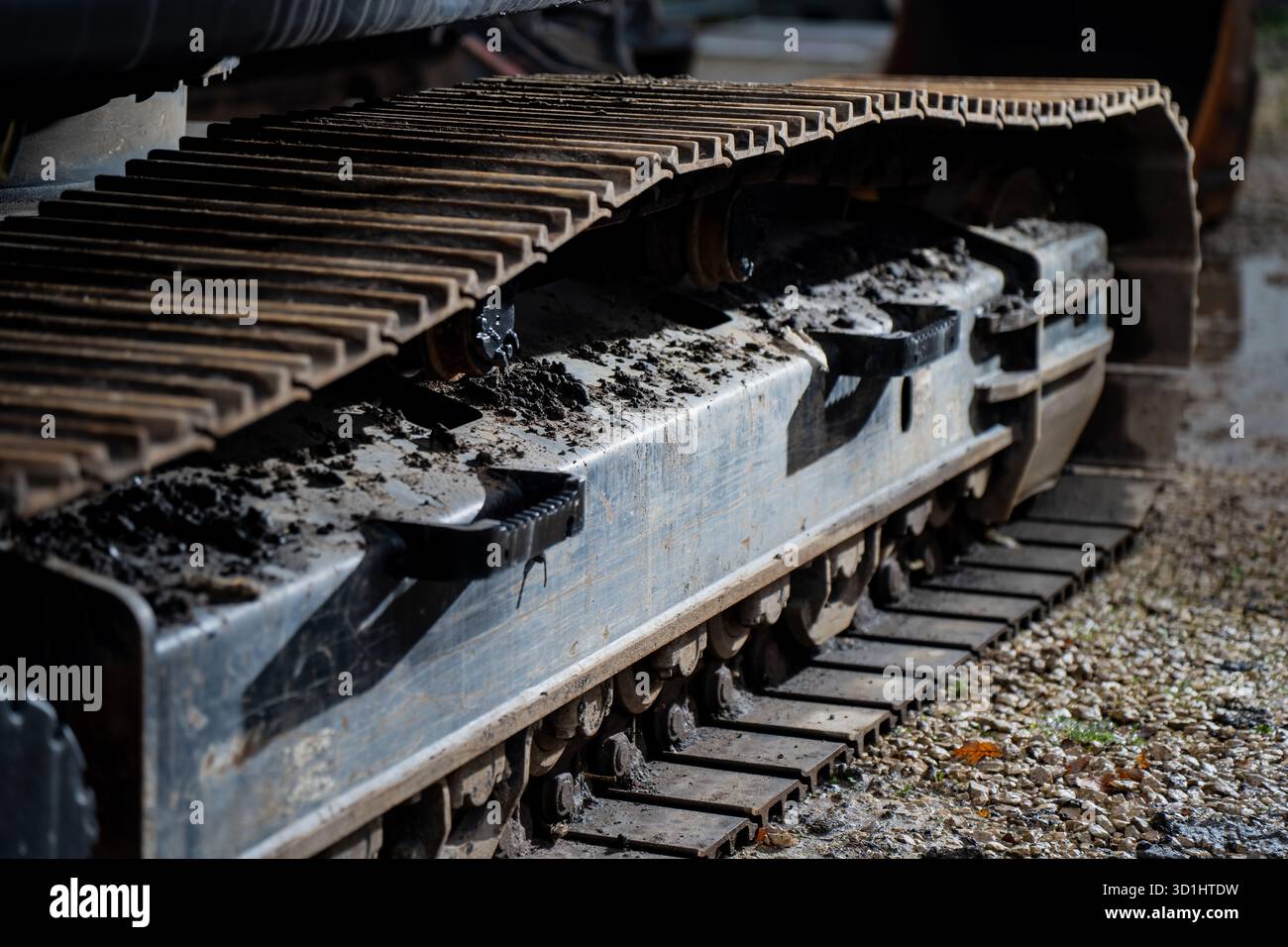 Heavy-duty excavator tracks coated with dirt on gravel surface ...