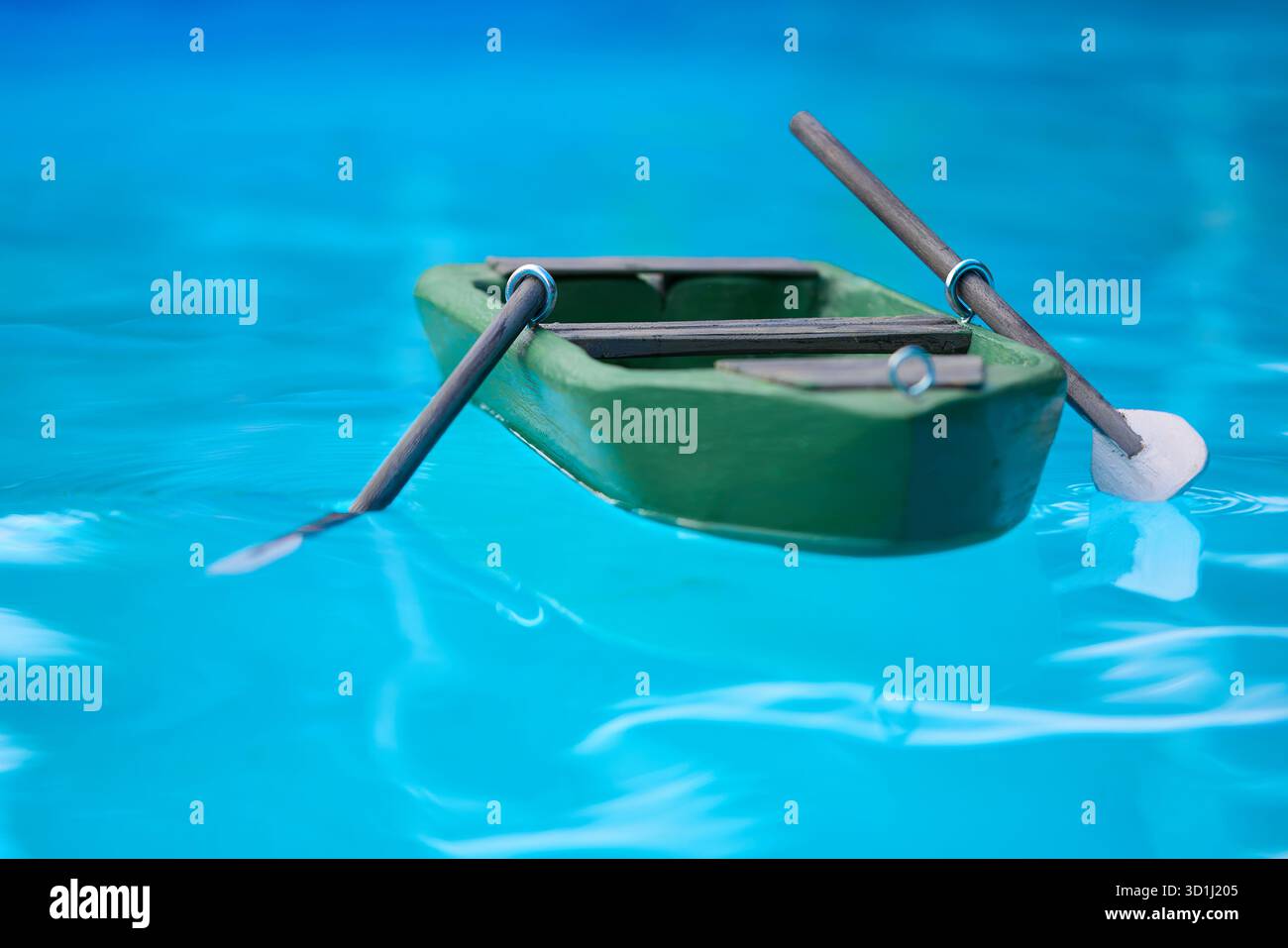 Wooden carved model of small punt with oars floating on level of pool ...