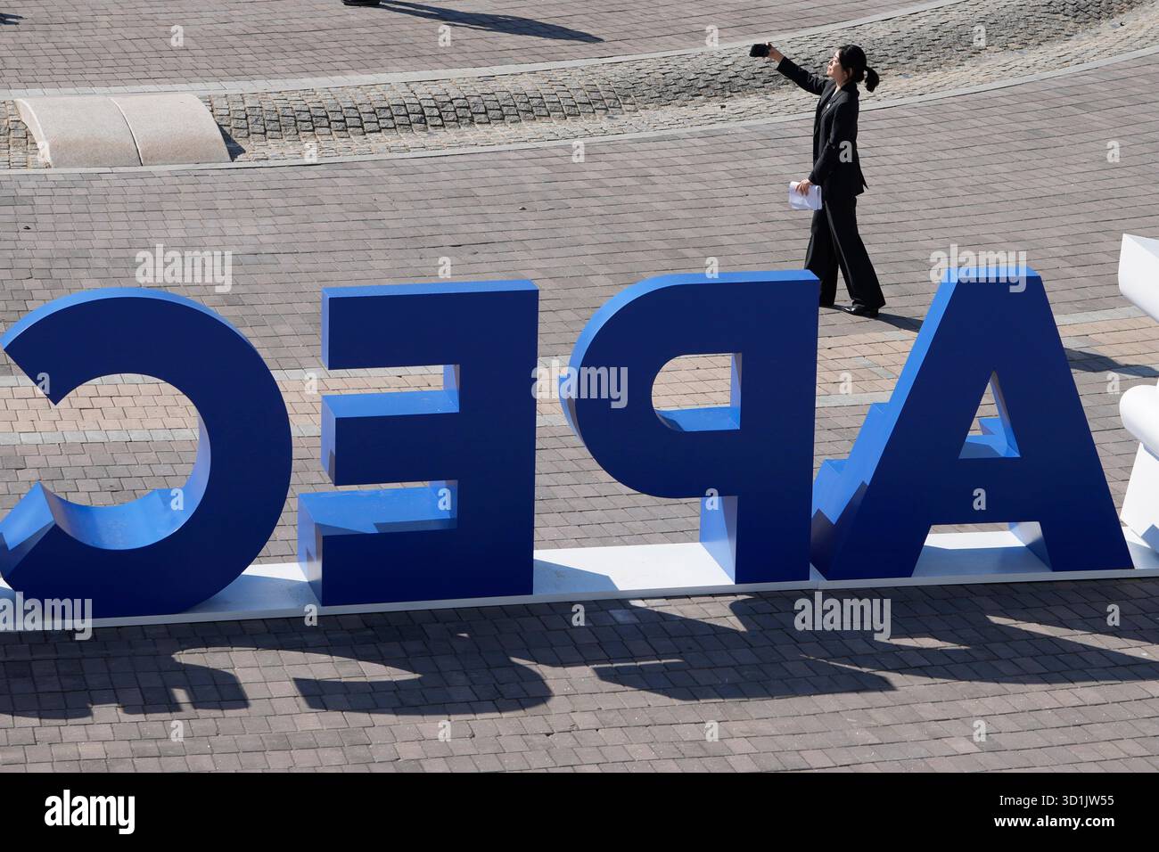 A woman takes a photo near a logo for the Asia-Pacific Economic ...