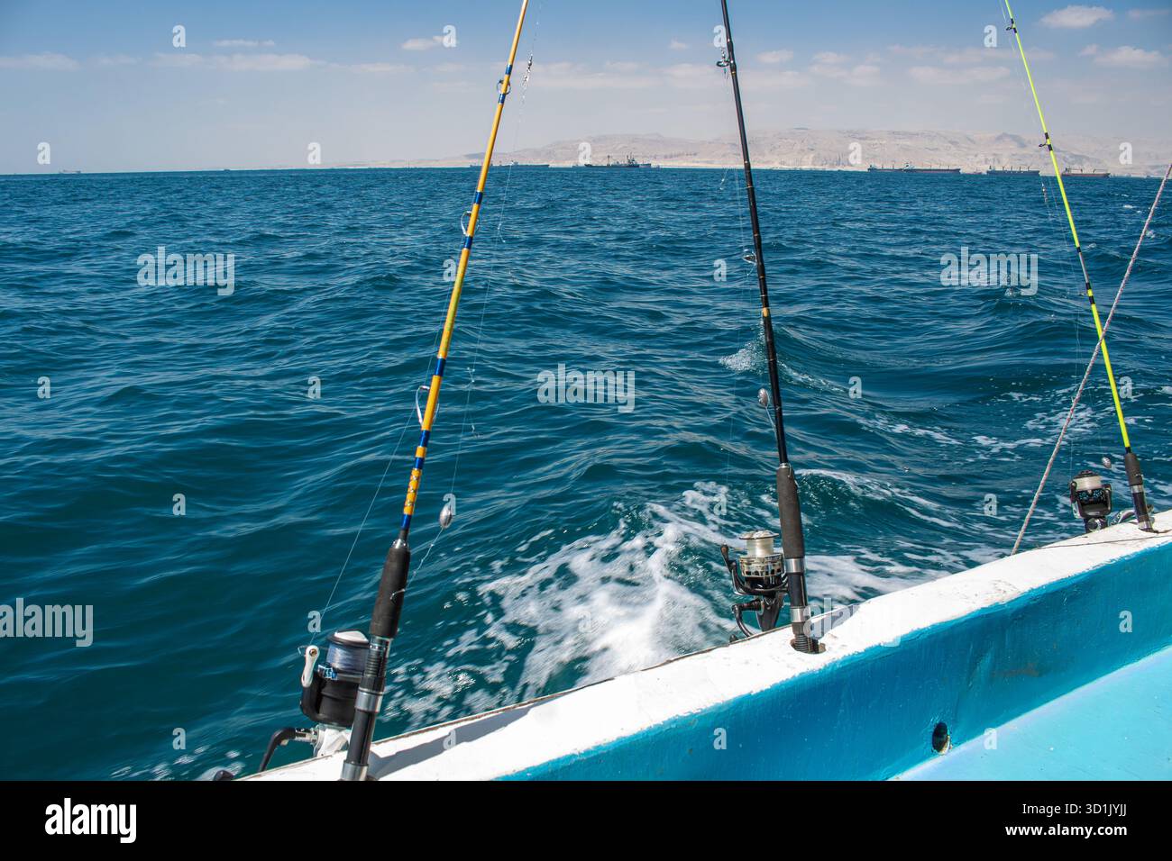 Three colorful fishing rods are set for trolling from the back of a ...