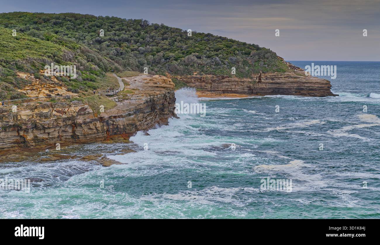 Waves breaking over cliff edges on rocky shoreline with headland in ...