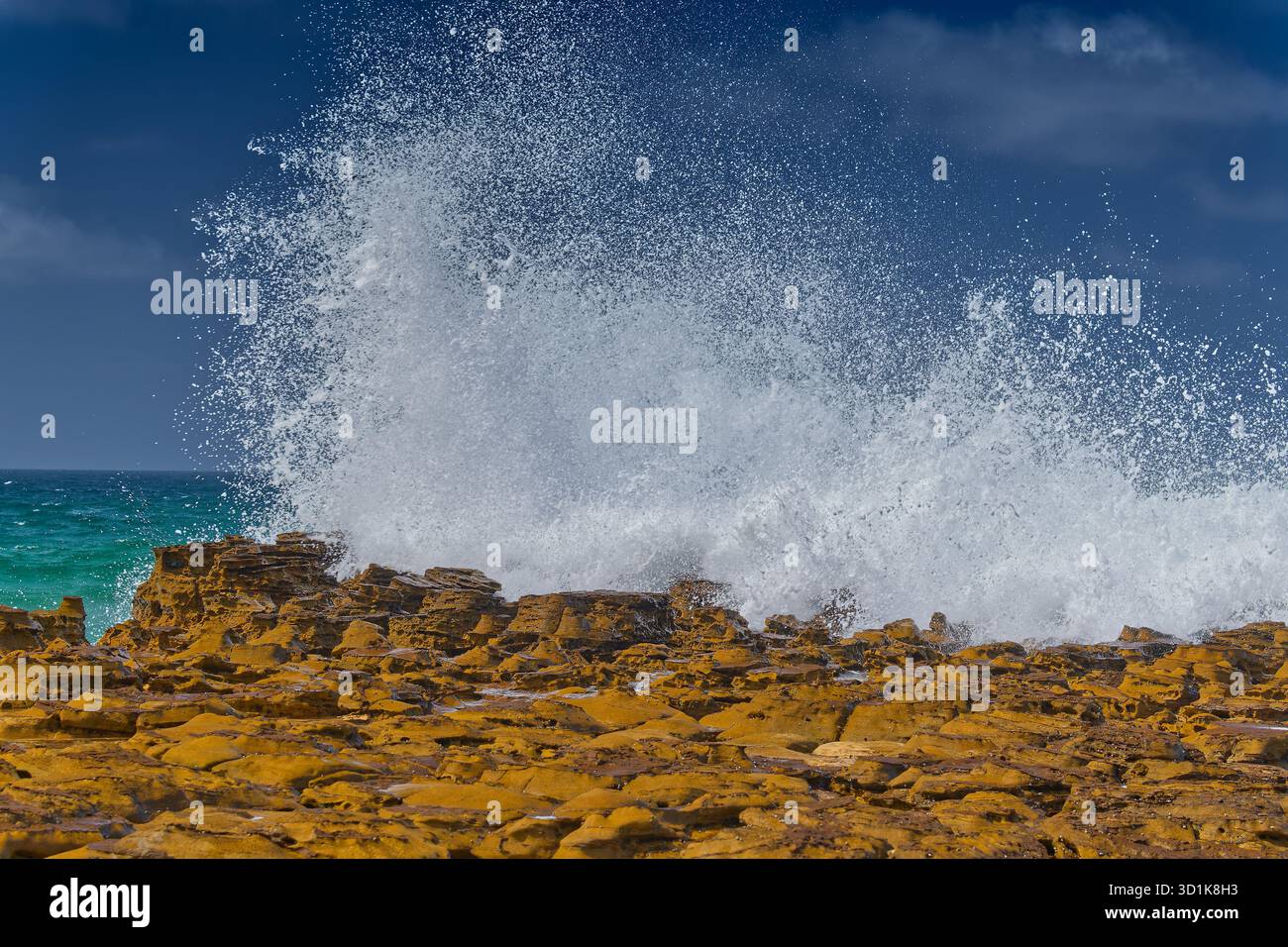 White wave breaking on rock platforms spraying white foam on sunny day ...