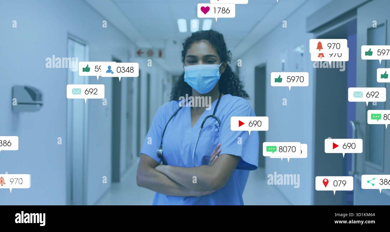 Standing mask wearing nurse crossing arms in hospital corridor, with ...