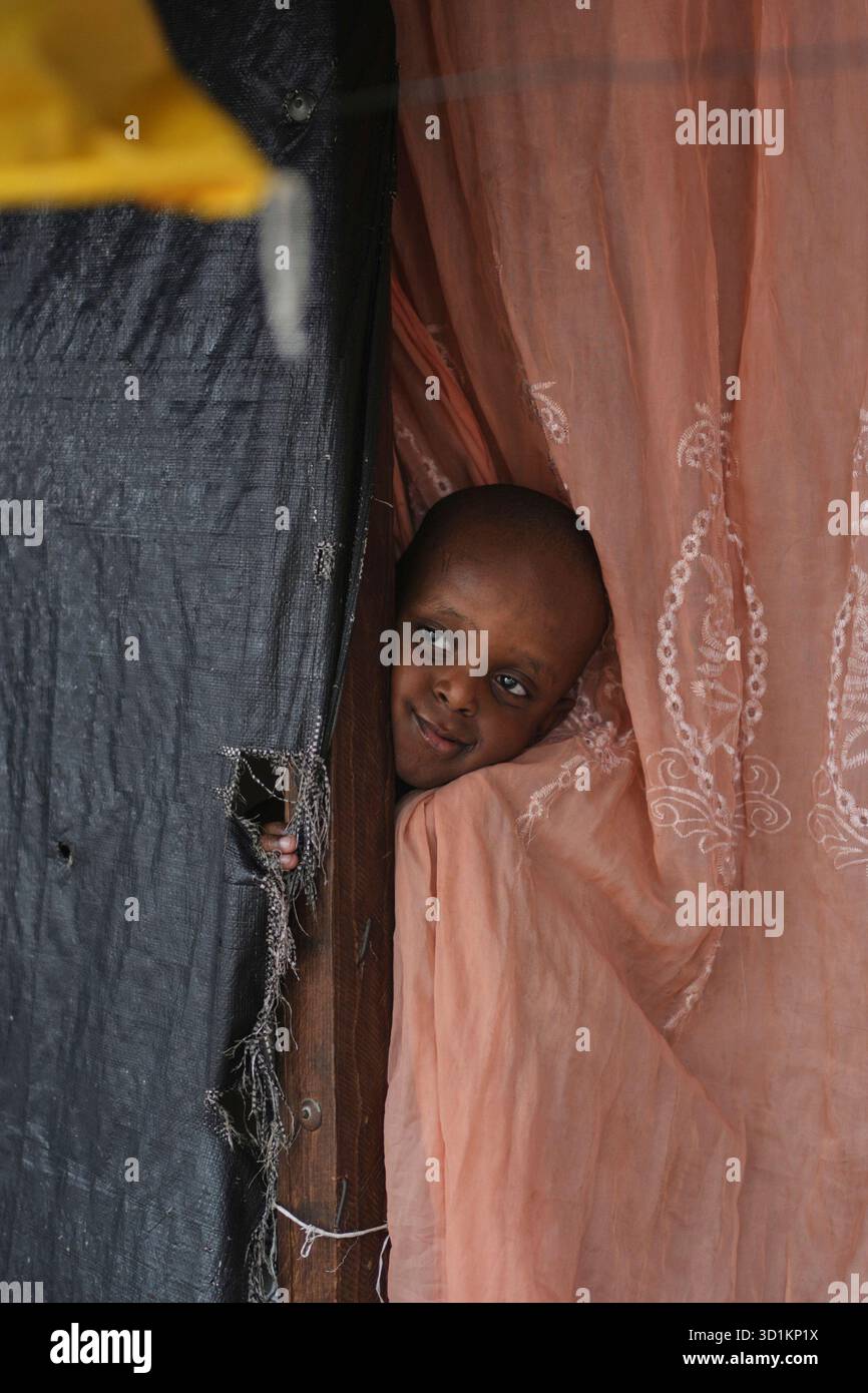 FILE - A child pokes his head out from behind a curtain at a shelter ...