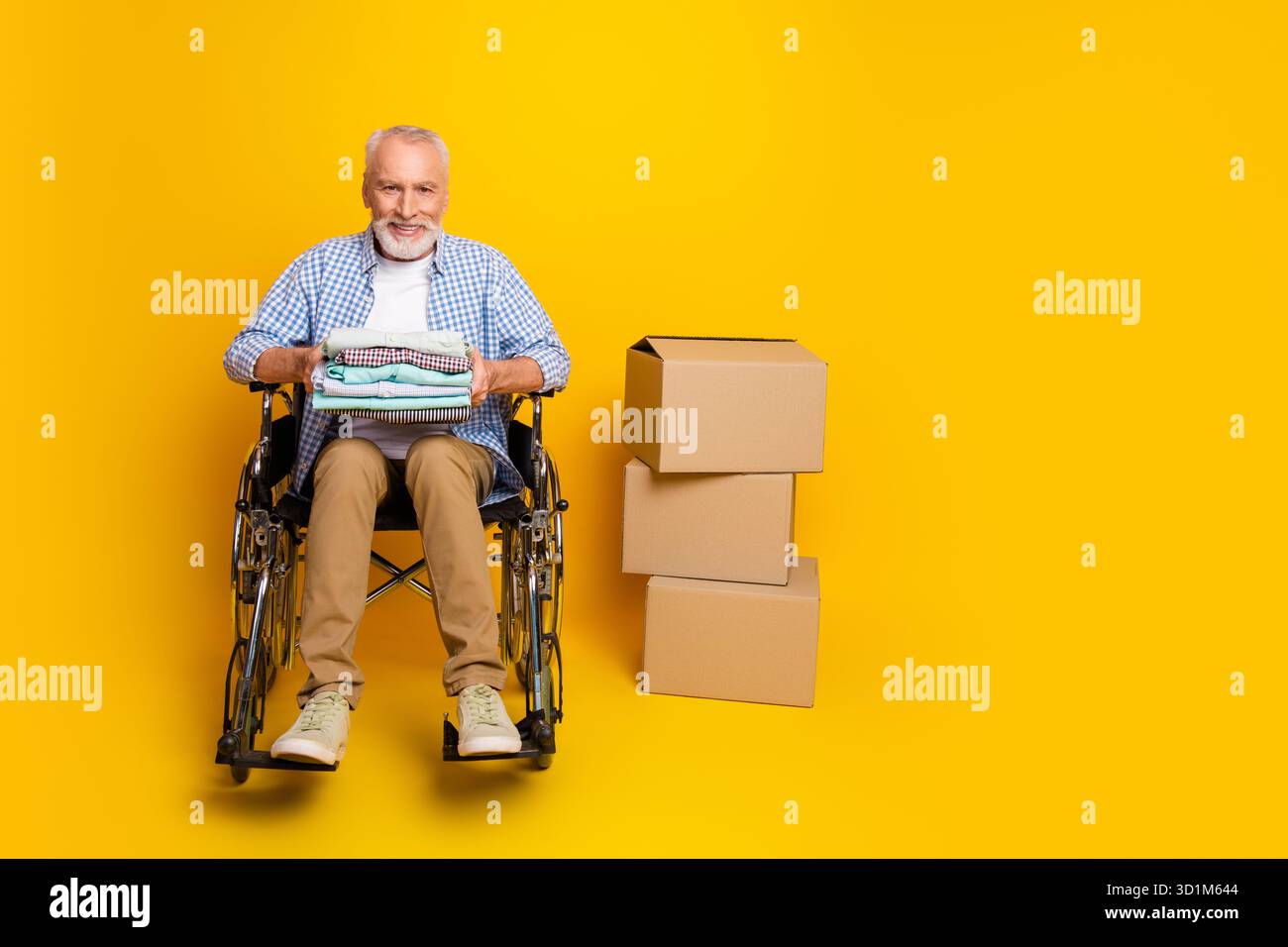 Cheerful grandpa in a wheelchair packs clothes and stacks moving boxes ...