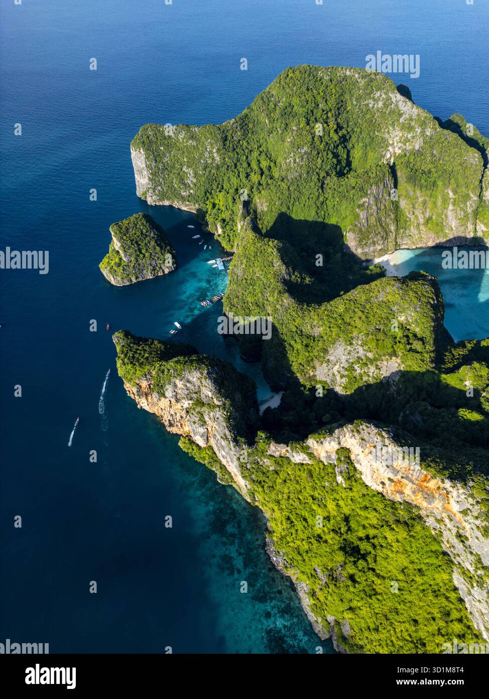 Aerial view of emerald waters embrace rugged, jungle-crowned cliffs ...