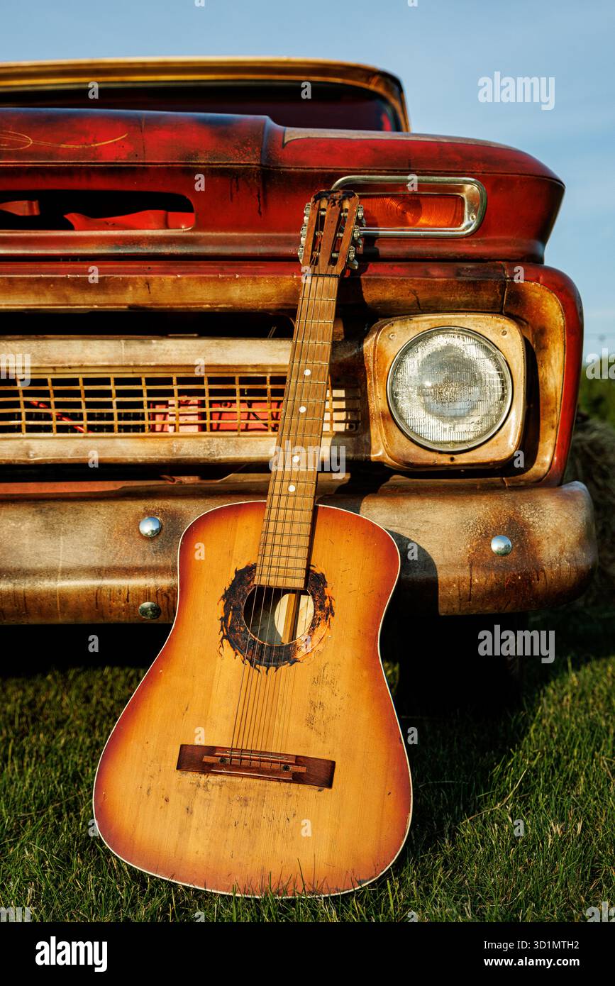 Old acoustic guitar resting against the front of a rusty red pickup ...