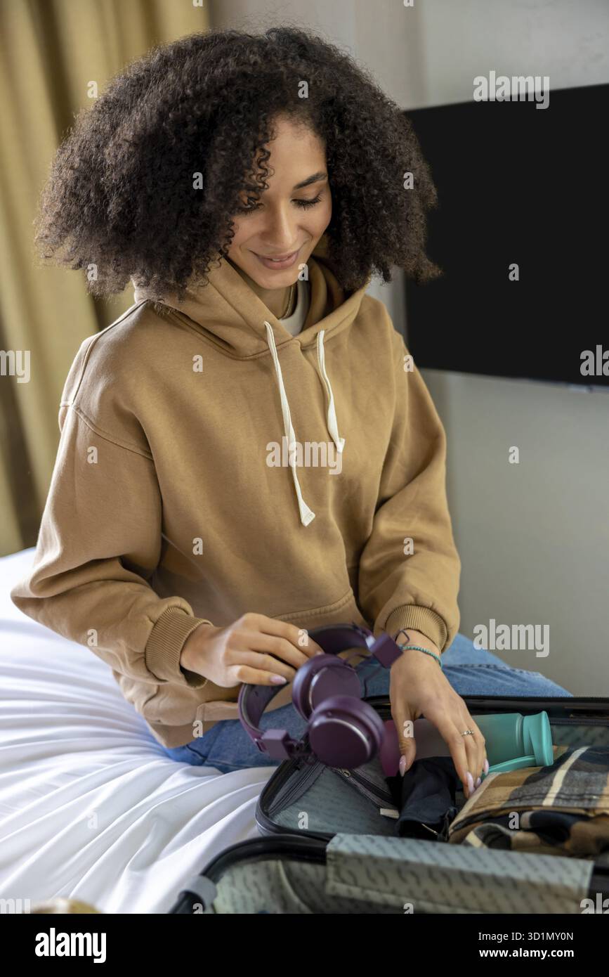 Ready for vacation. Curly-haired pretty young woman packing her ...