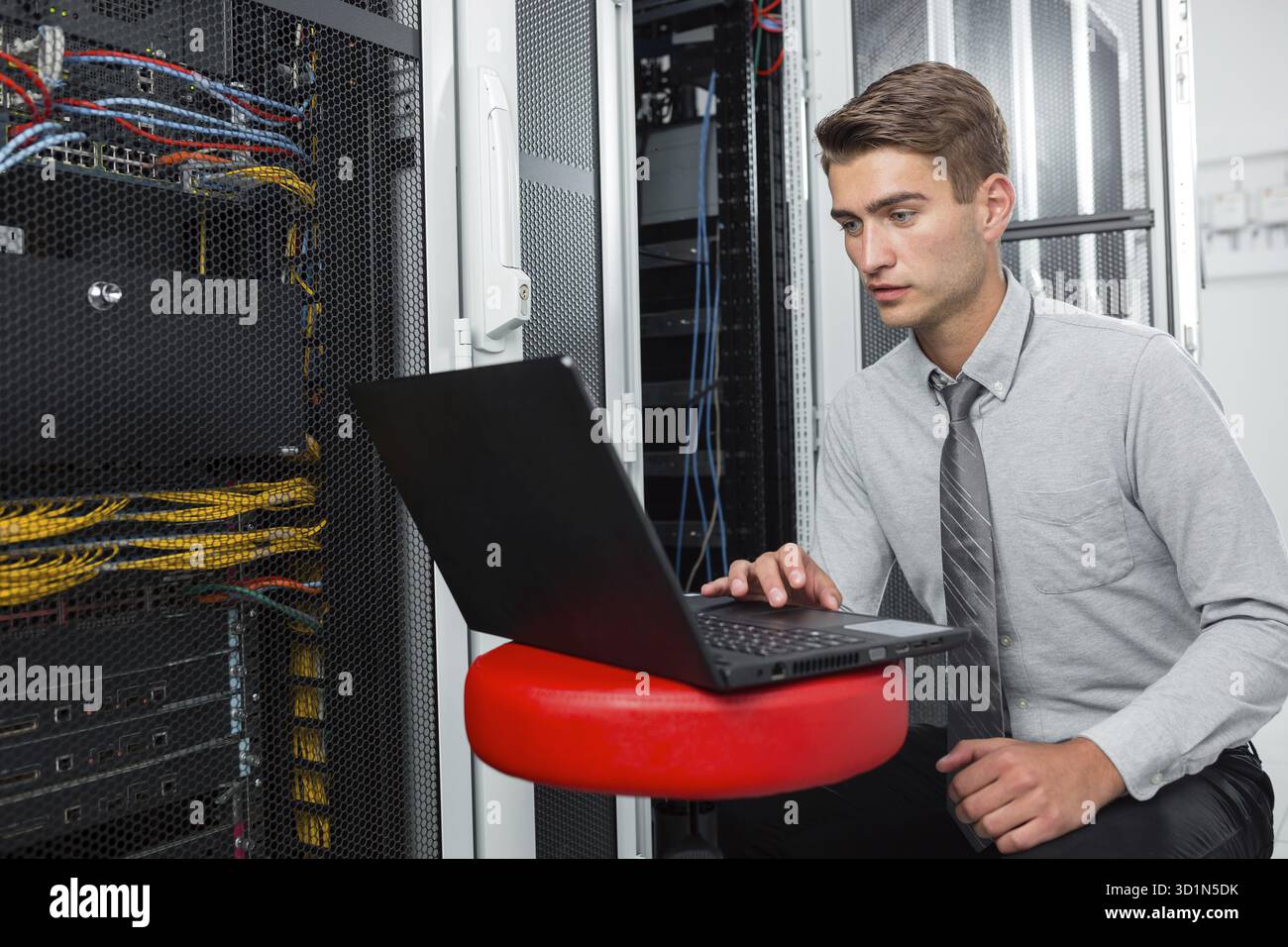 Portrait of modern young man holding laptop standing in server room ...