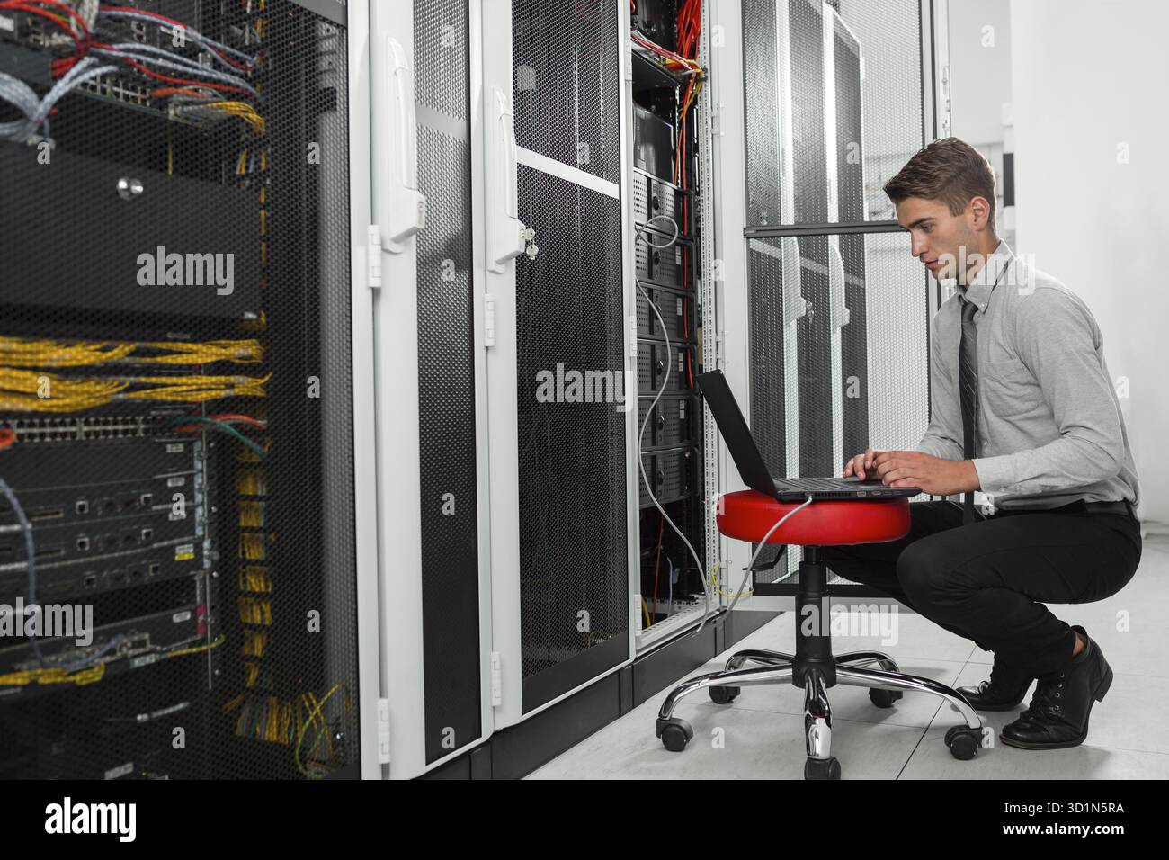 Portrait of modern young man holding laptop standing in server room ...