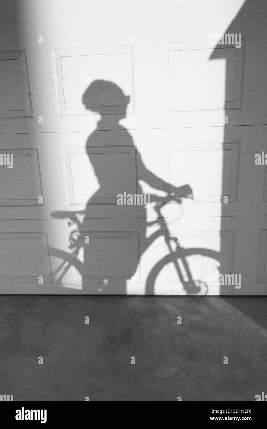 Shadow of a woman riding a bike on a textured wall. Two tonal image ...