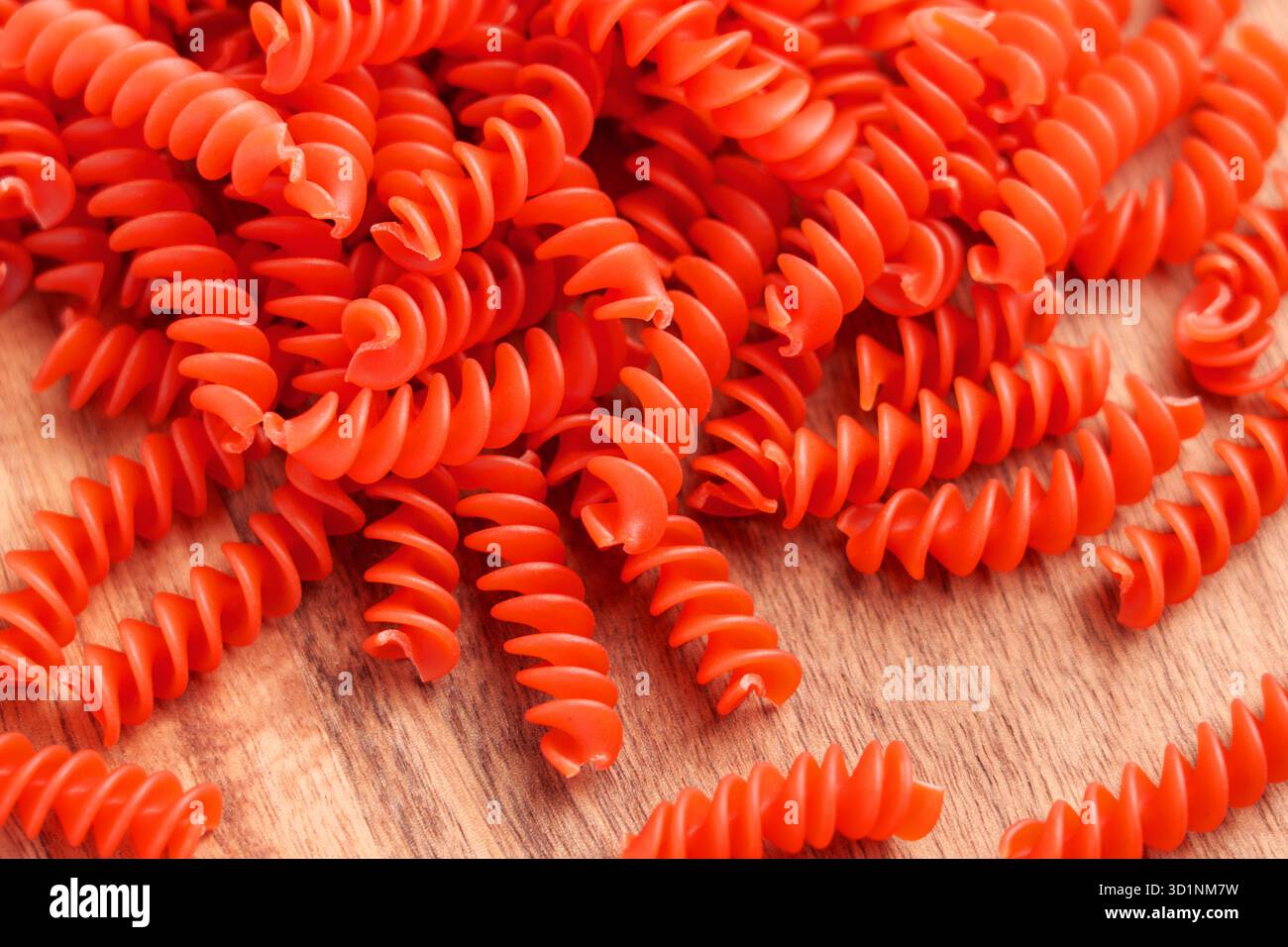 Uncooked red lentil fusilli pasta scattered on a wooden texture close ...