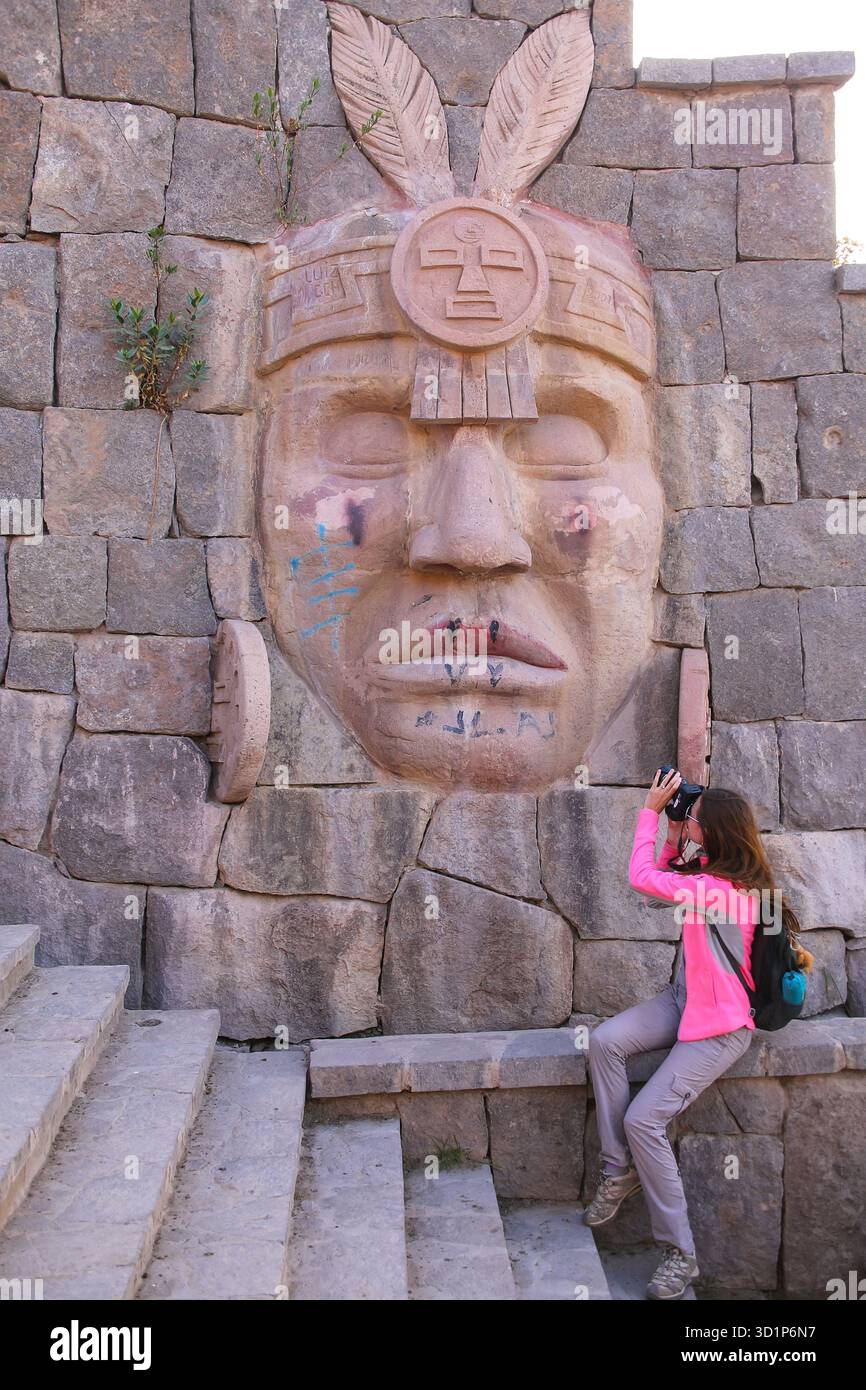 Woman photographing carving of Inca warrior on a wall in Chivay town ...