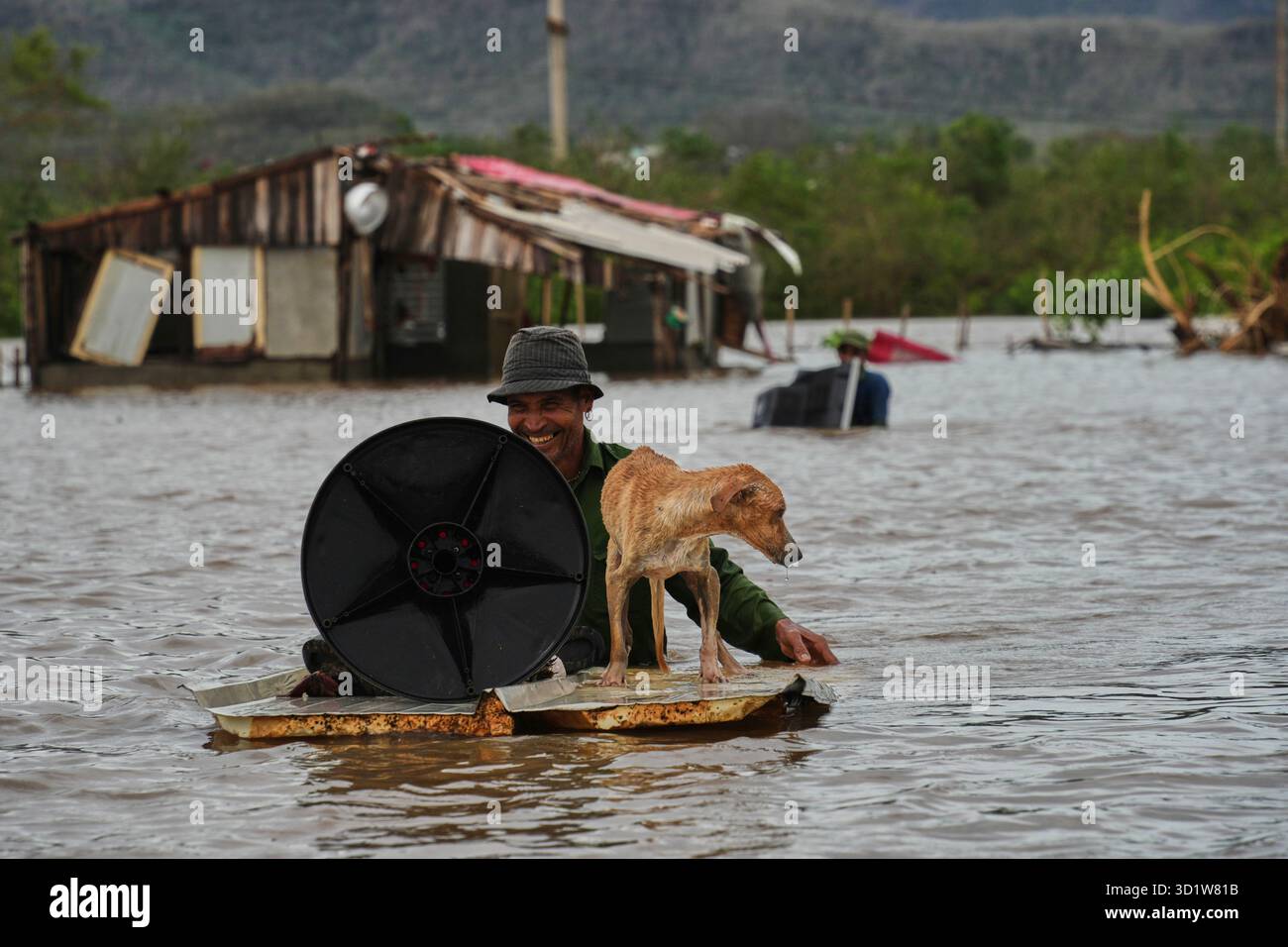 A man wades through floodwaters with his dog and belongings from his ...