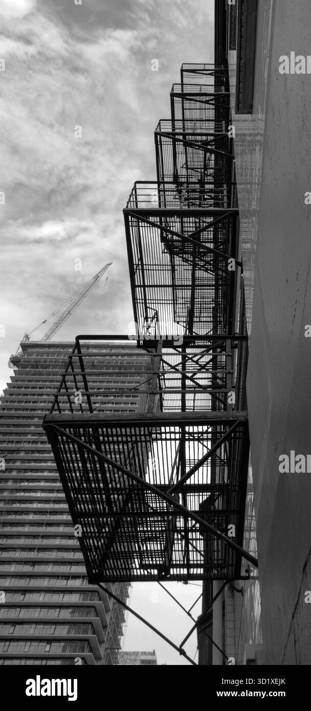 Looking up at fire escape attached to building as skyscrape is built in ...
