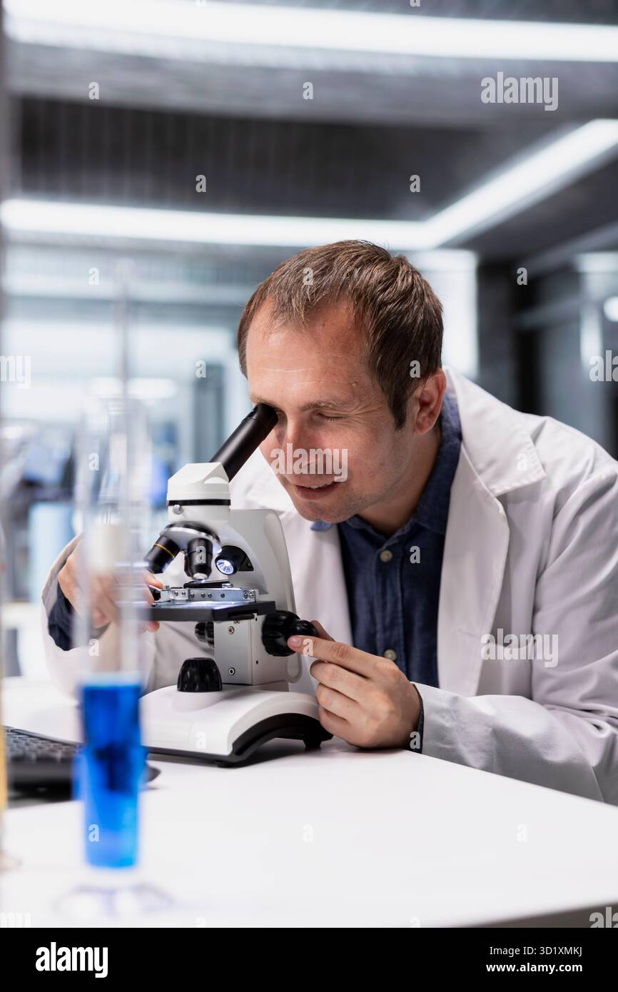 Male scientist evaluating specimen under microscope in clinical lab ...