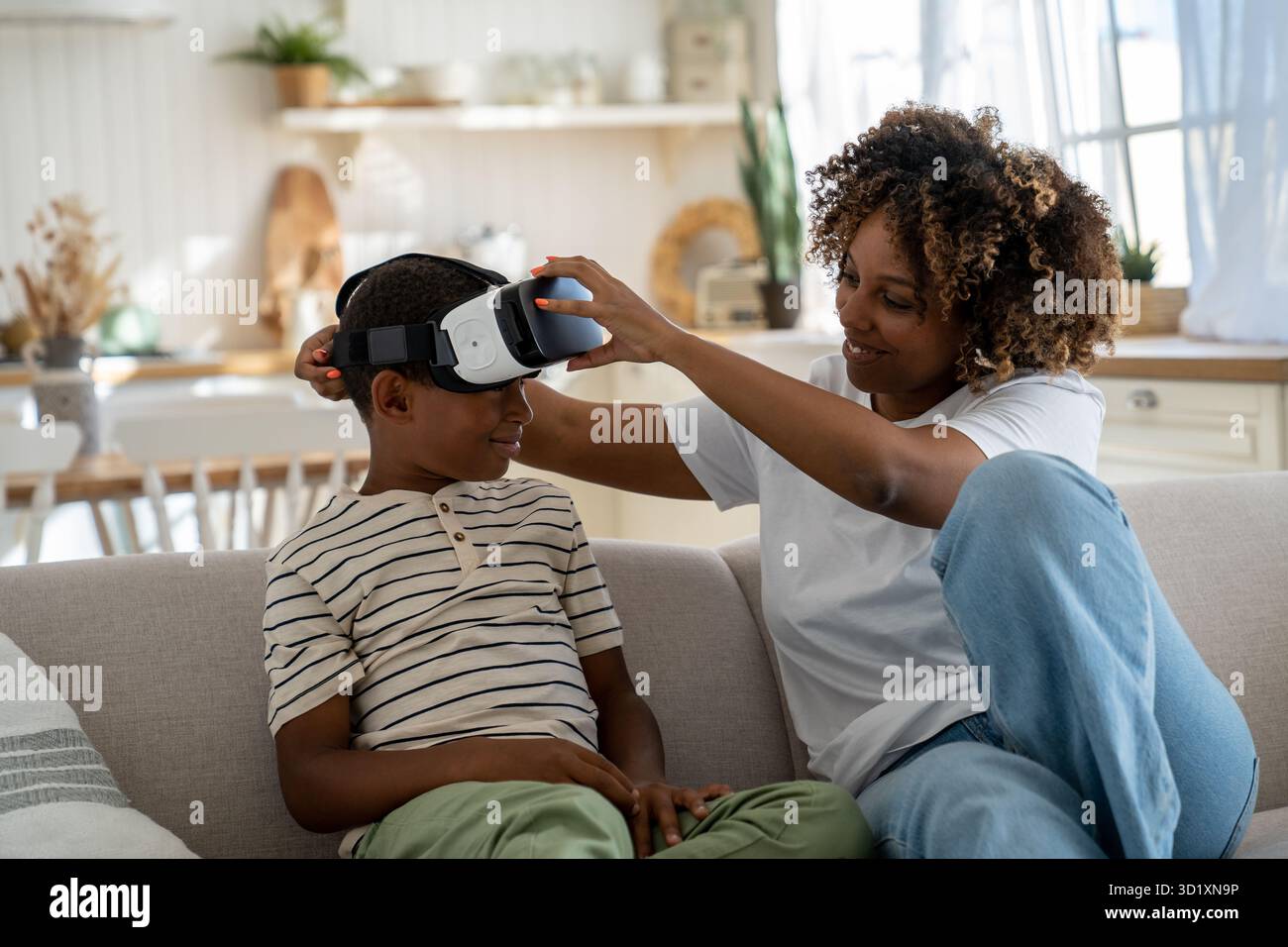 African American mom sitting with child son on sofa taking off his vr ...