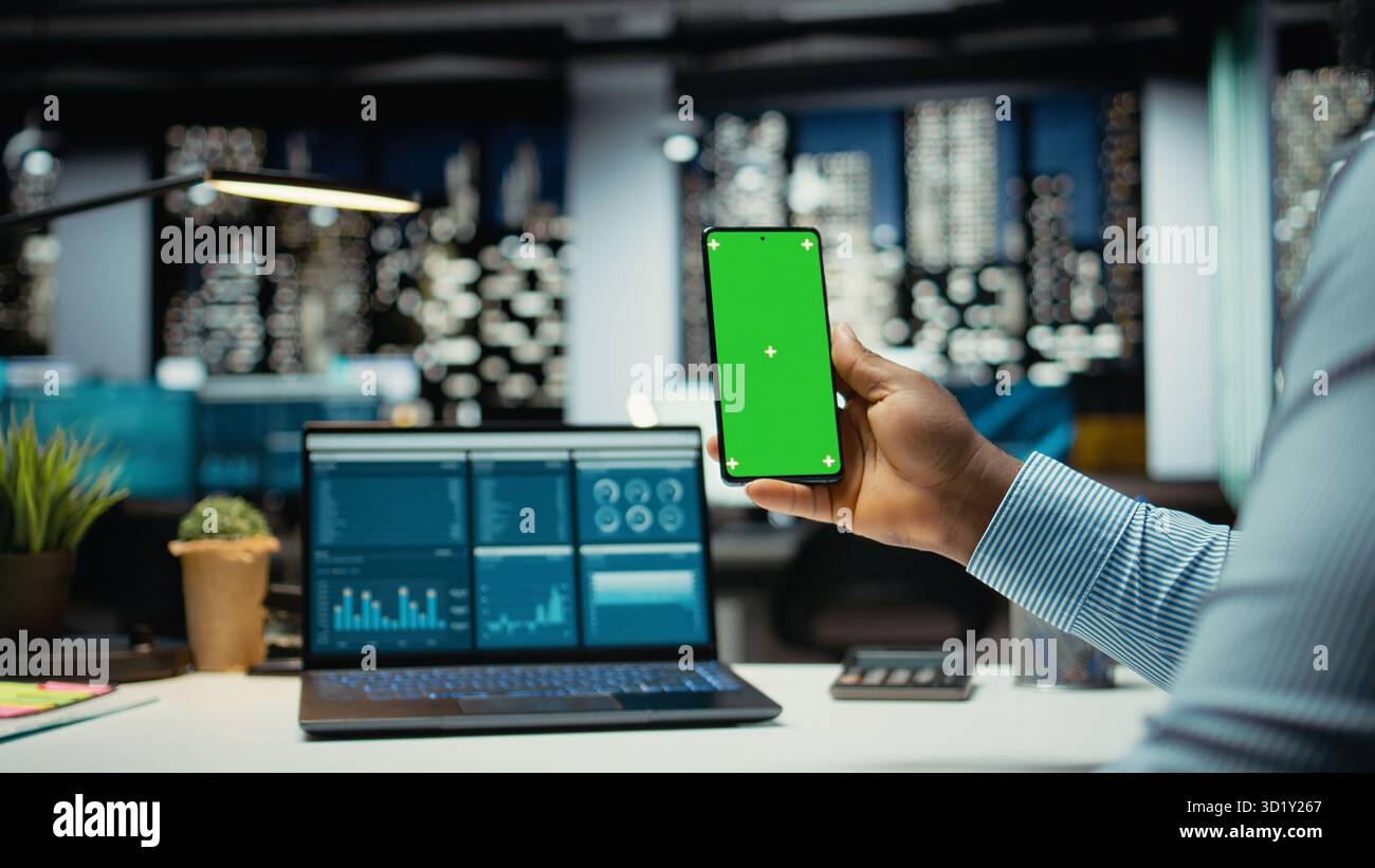 Black professional looks at chroma key on mobile phone screen at desk ...