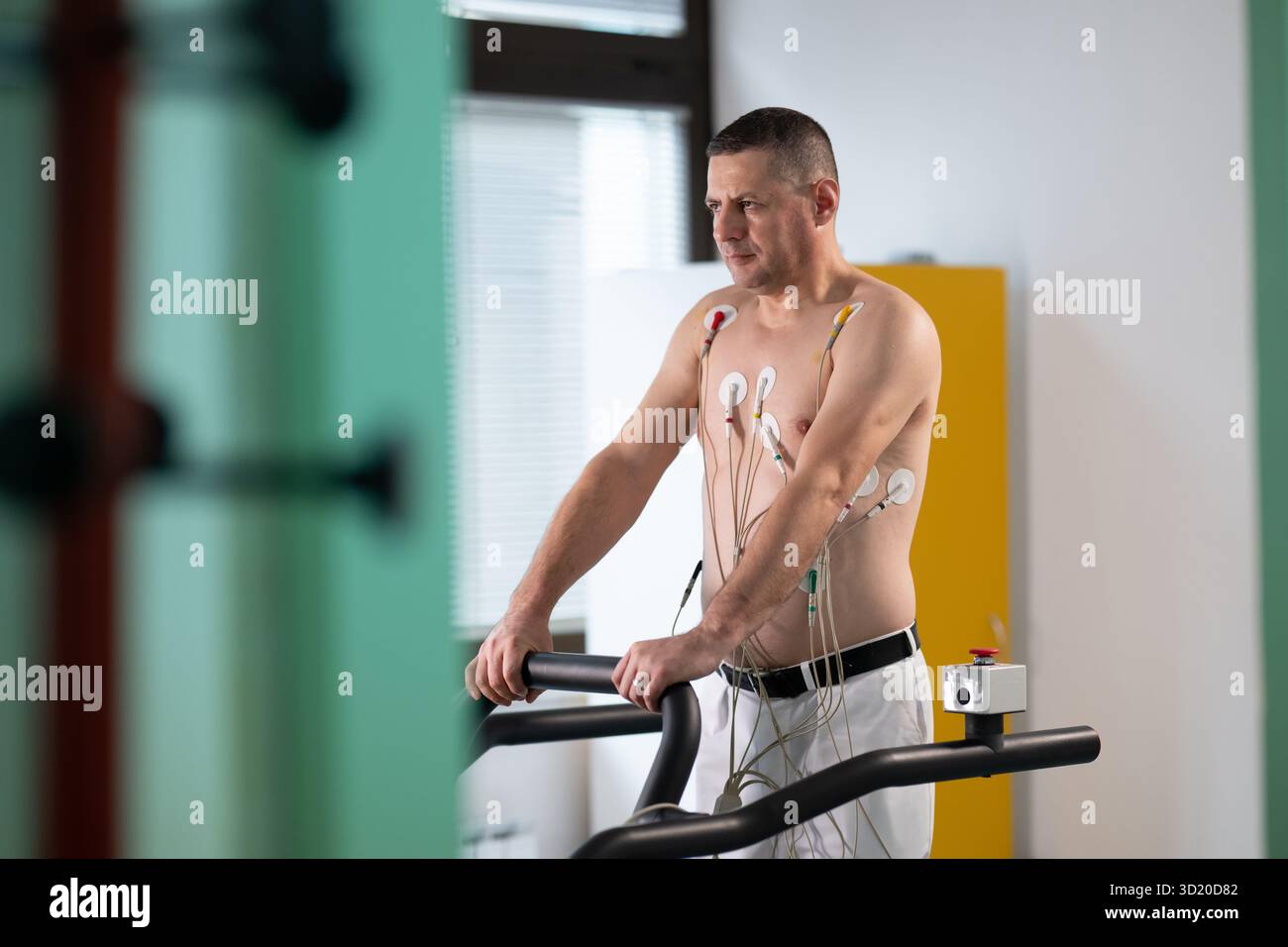 A middle-aged man is undergoing a medical stress test on a treadmill ...