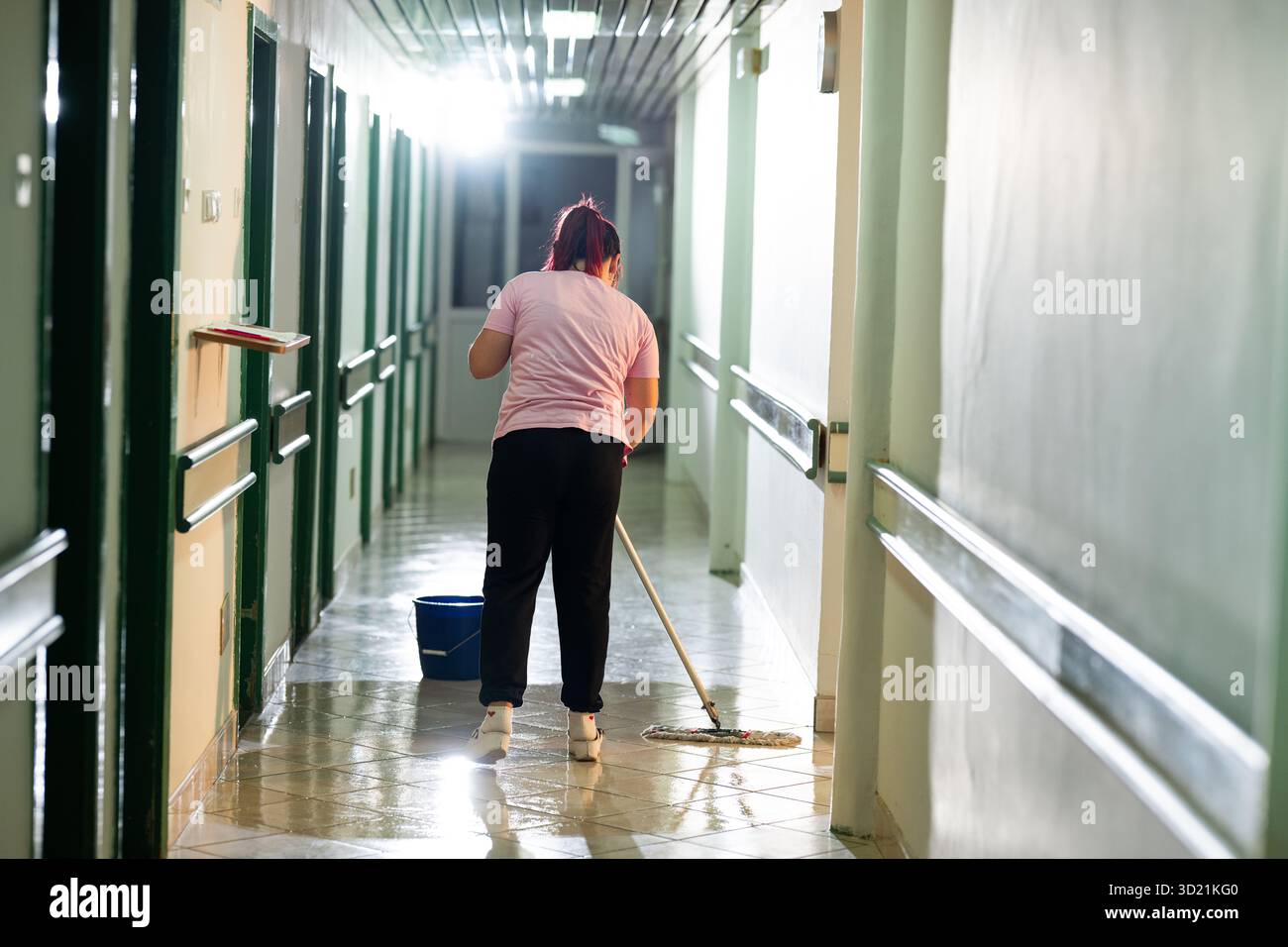 Female janitor standing in a hospital corridor with mop and bucket ...
