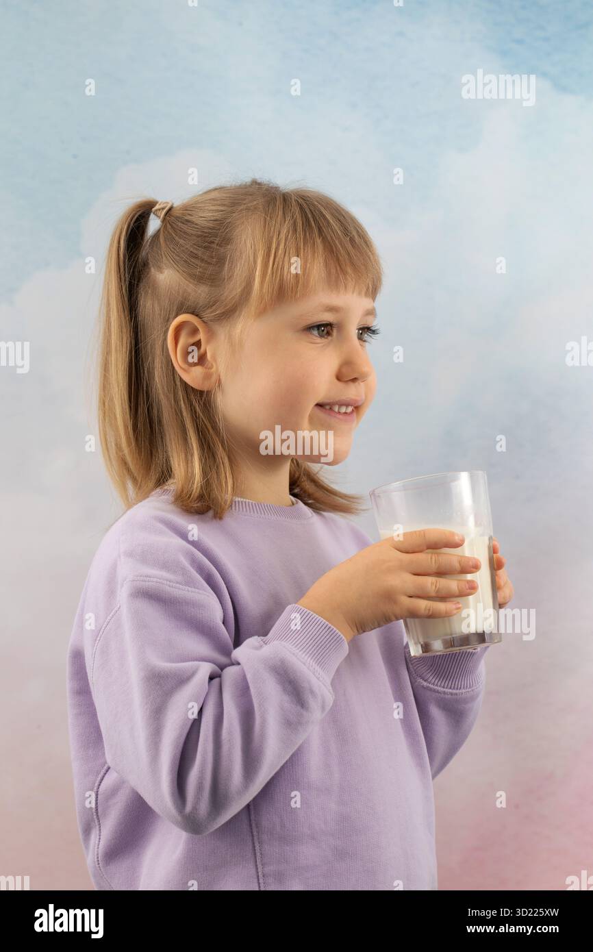 Happy junior schoolgirl holds glass of milk after drinking. Mom gives ...