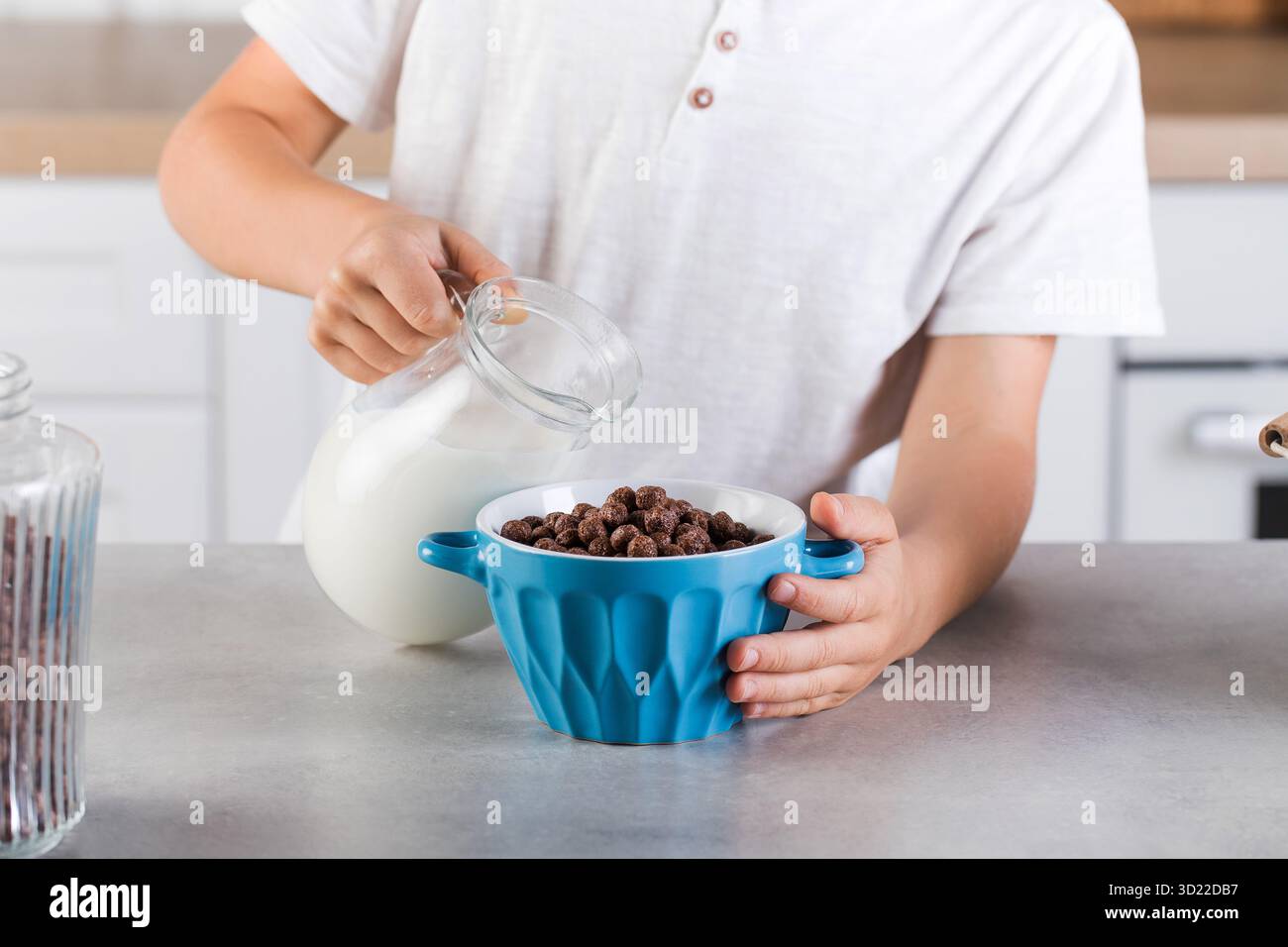 A child pours milk from a jug into a bowl of chocolate flakes. Child's ...