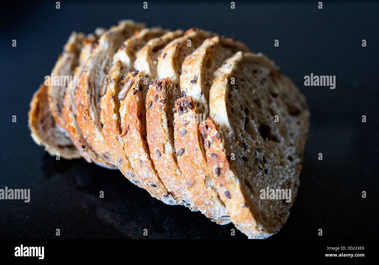 Rustic wholegrain bread loaf with crispy crust on black surface ...