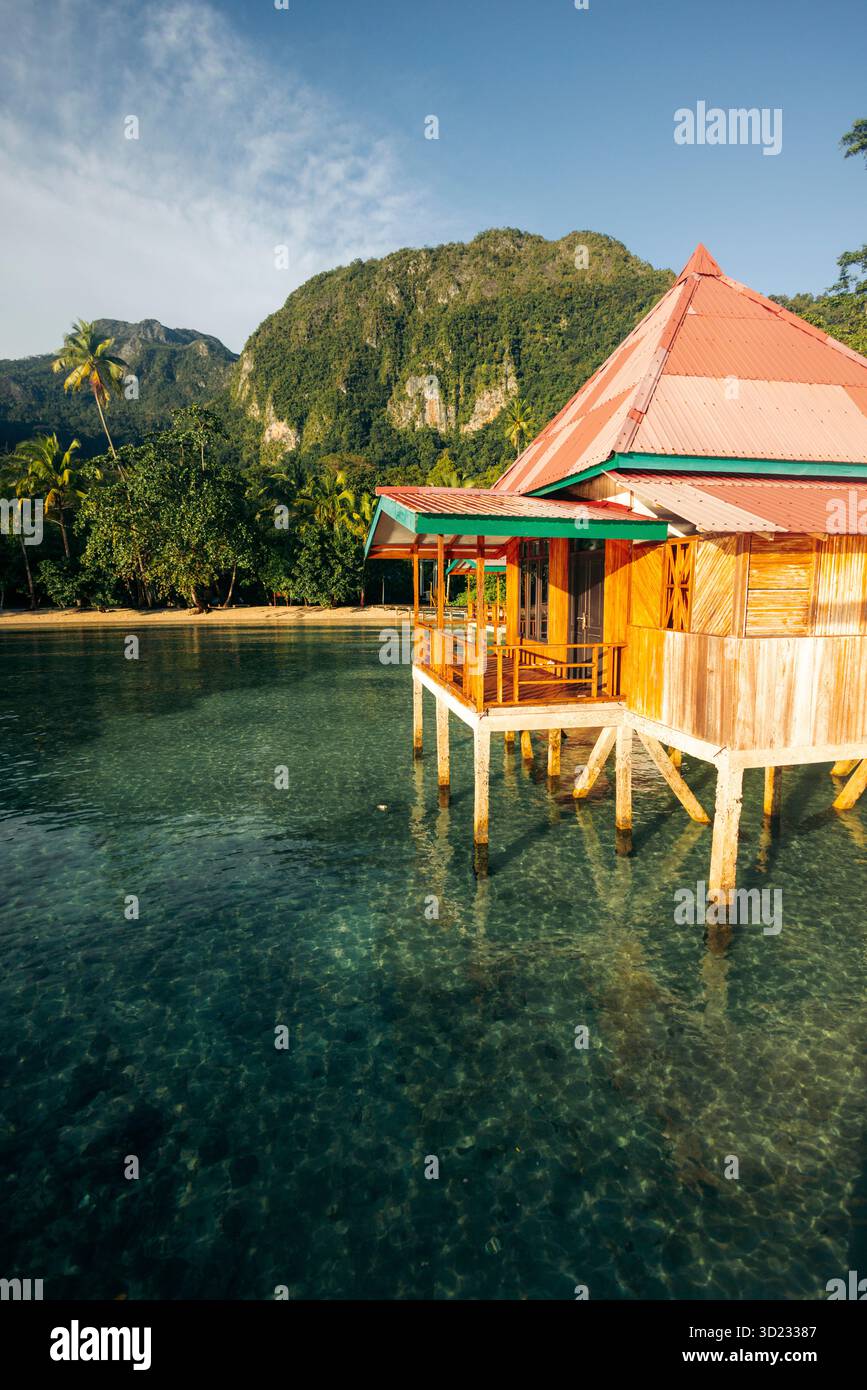 Wooden stilt house over clear blue water with lush green mountains in ...