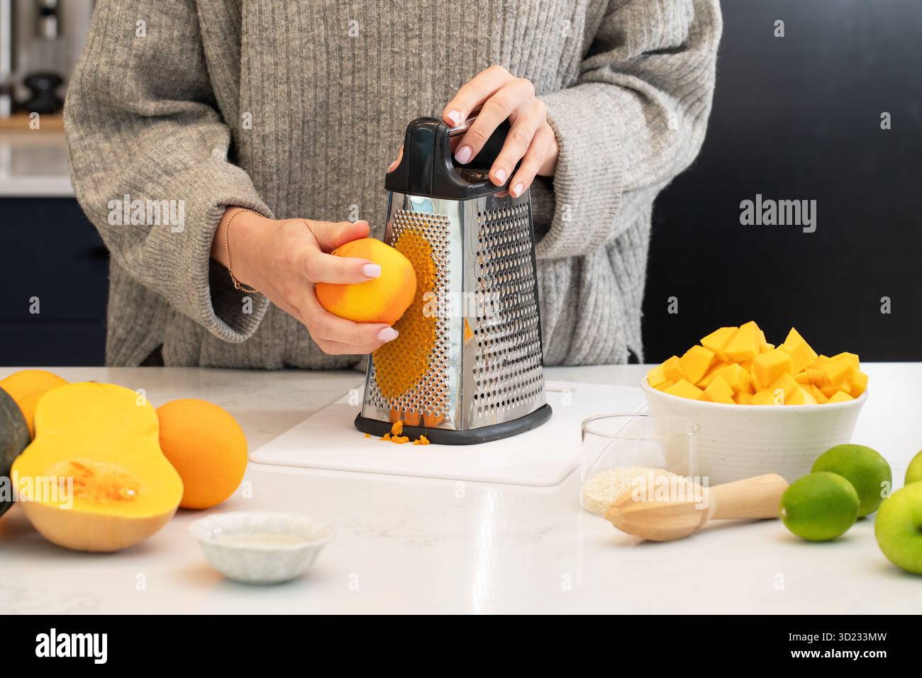 Caucasian adult grating fresh orange in kitchen with fruit selection ...