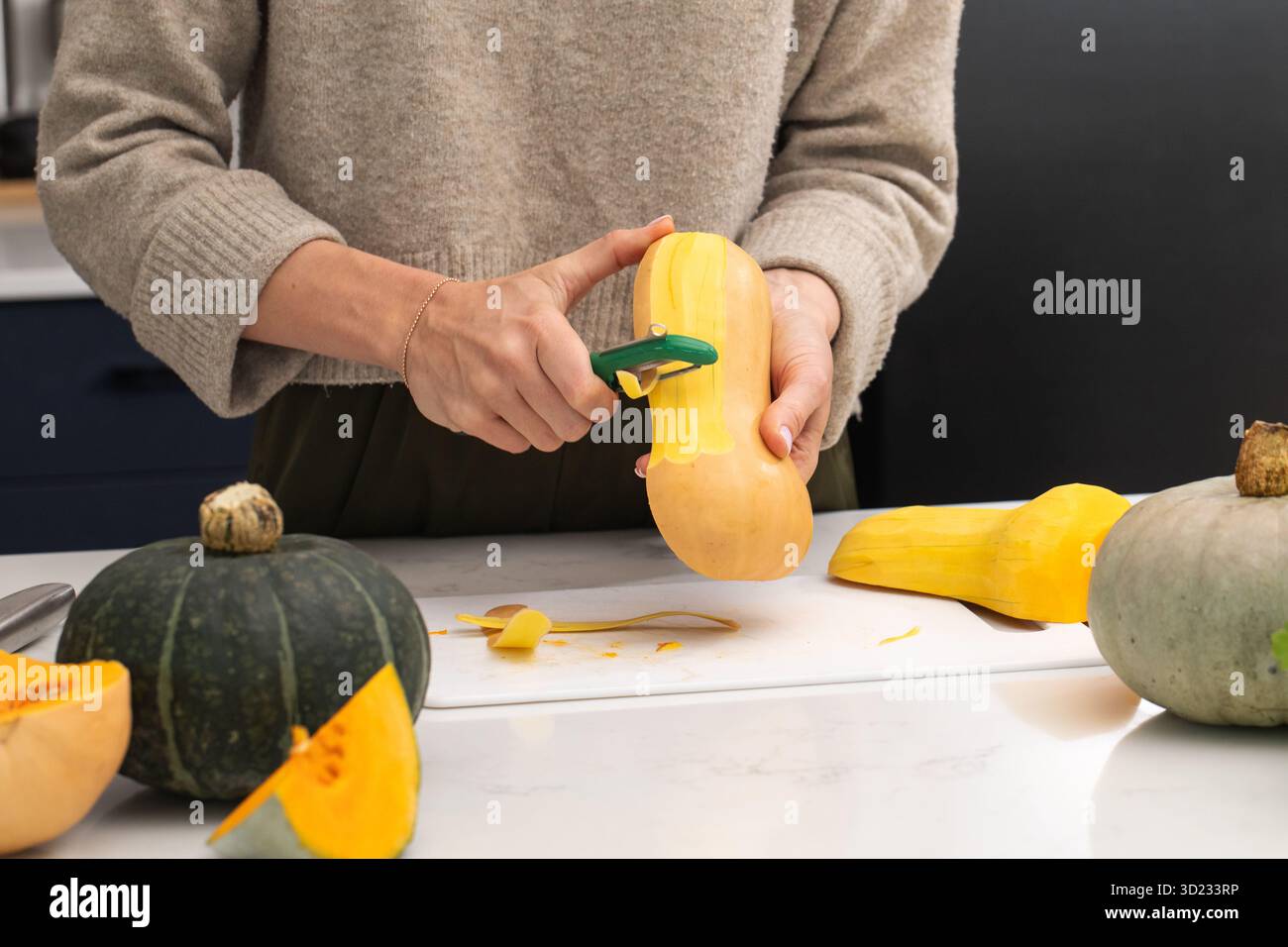 Female adult peeling butternut squash in kitchen with varieties of ...