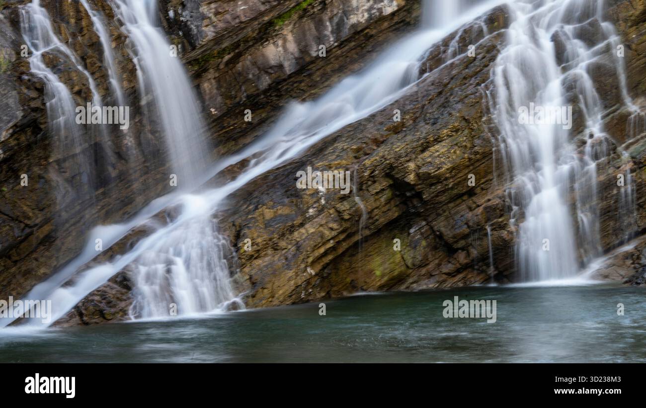 Cascading waterfalls flow over layered rocky cliffs into a calm, clear ...