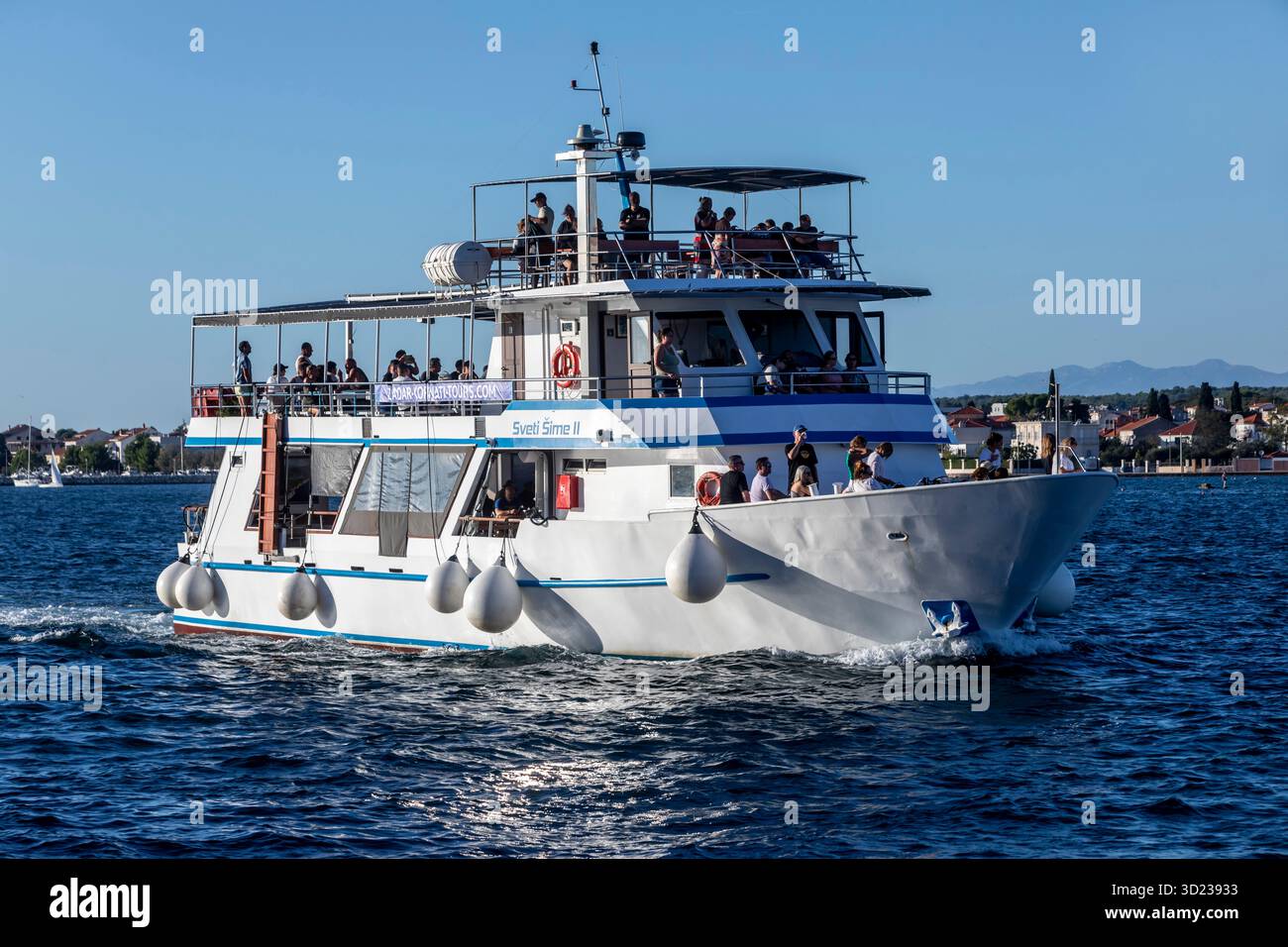 A white tourist boat with multiple decks sails on a sunny day with ...