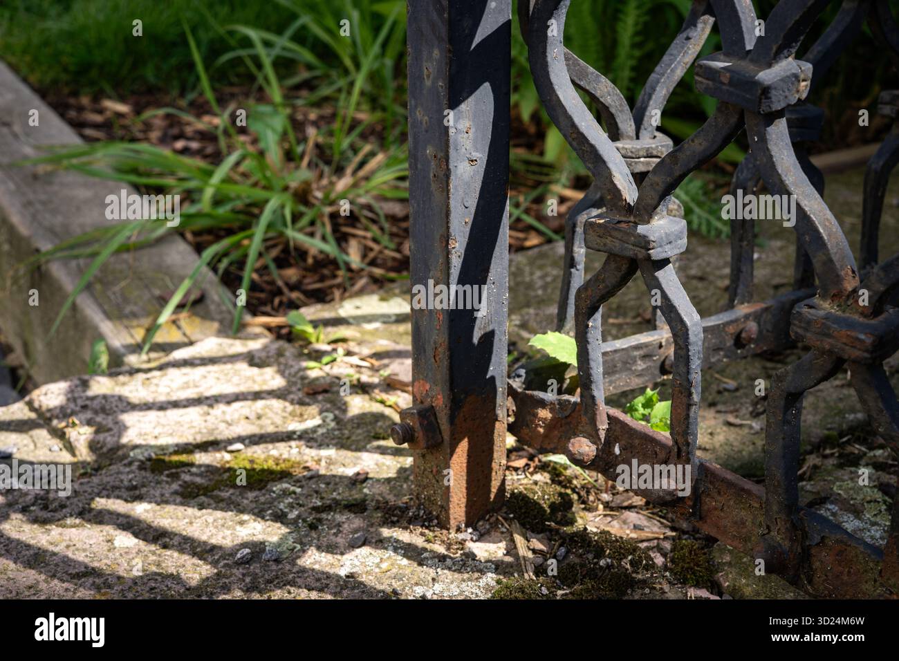 Detail of an old wrought iron fence casting a shadow on a mossy stone ...
