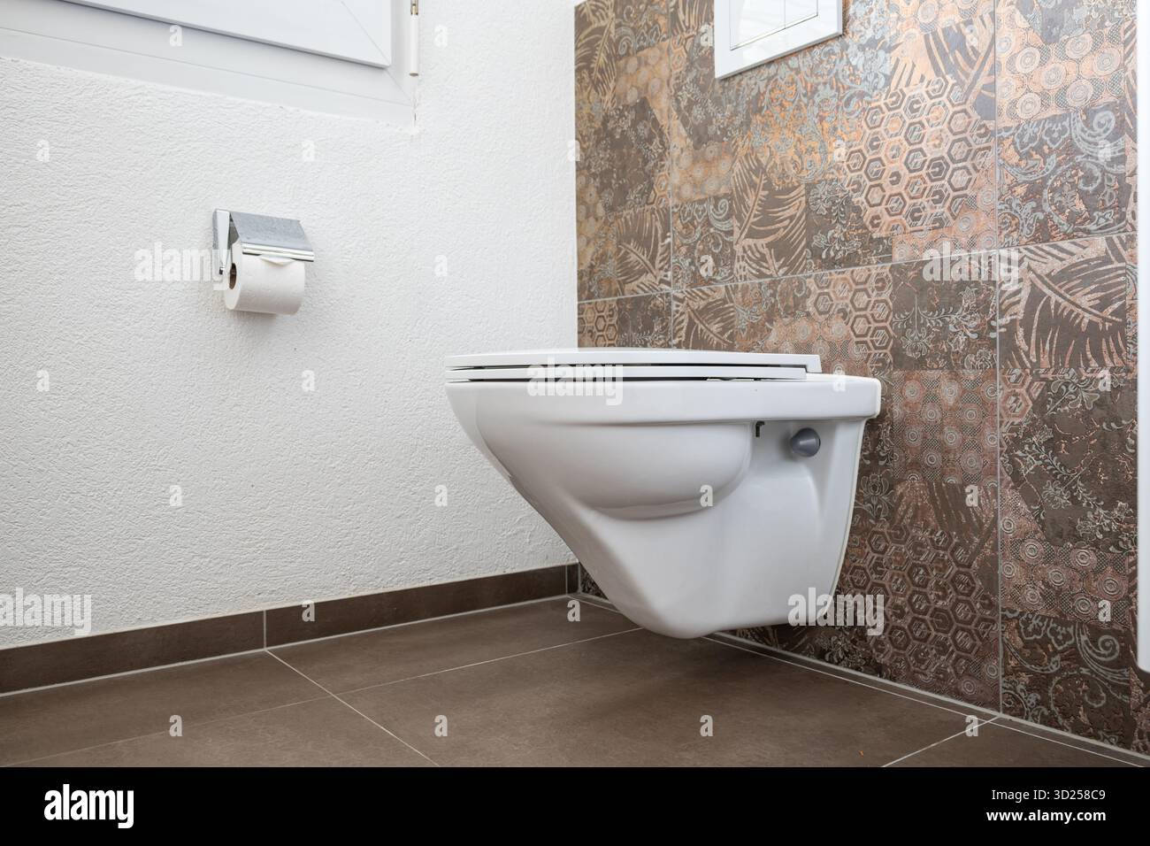 White ceramic toilet bowl inside modern bathroom with tiled floor and ...