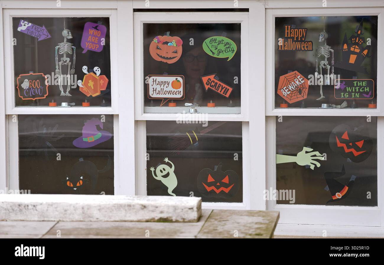 A woman peers through a Halloween themed decorated window of a house in ...