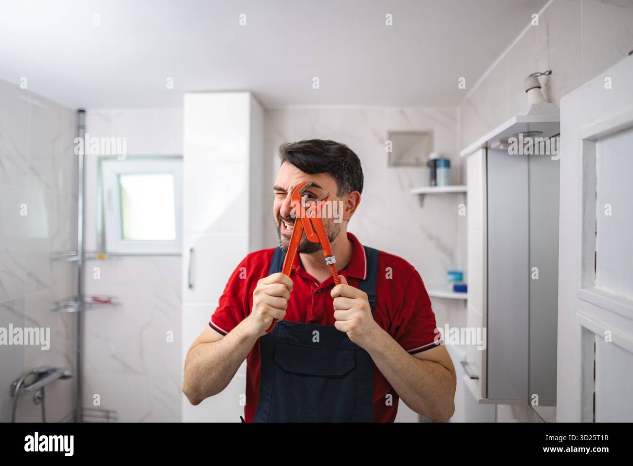 Plumber making funny face with pipe wrench in bathroom Stock Photo - Alamy