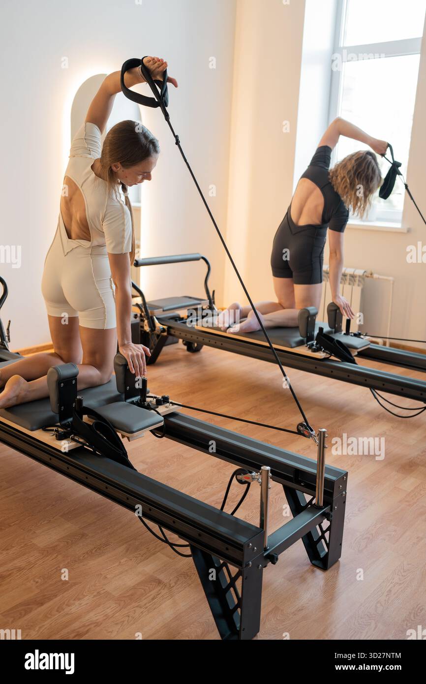 Split training of two girls adjusting reformer arm and core exercises ...