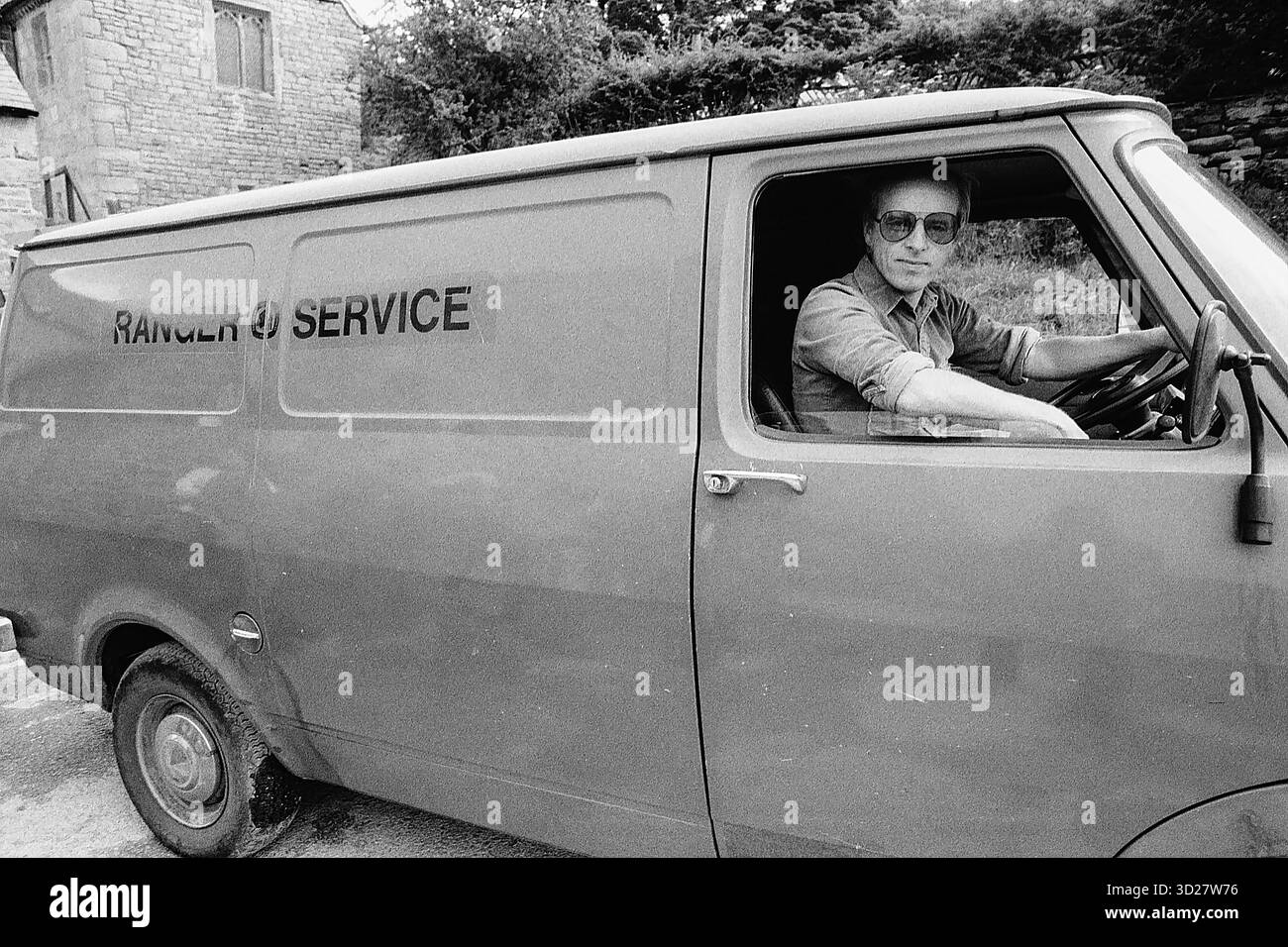 The image depicts a male park ranger driving a white van in the Peak ...
