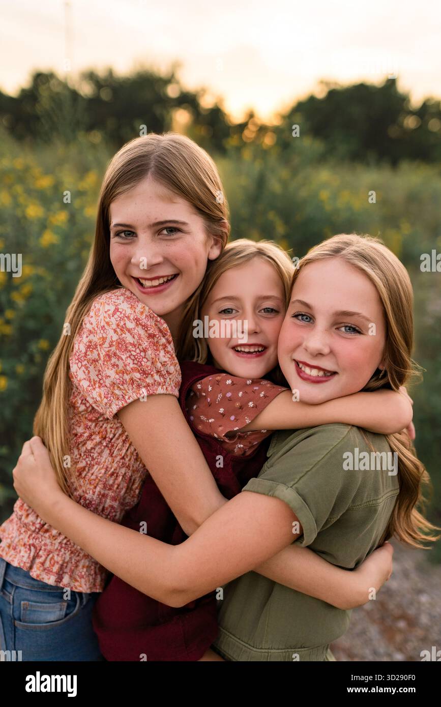 Three smiling girls hug closely in wildflower field at sunset Stock ...