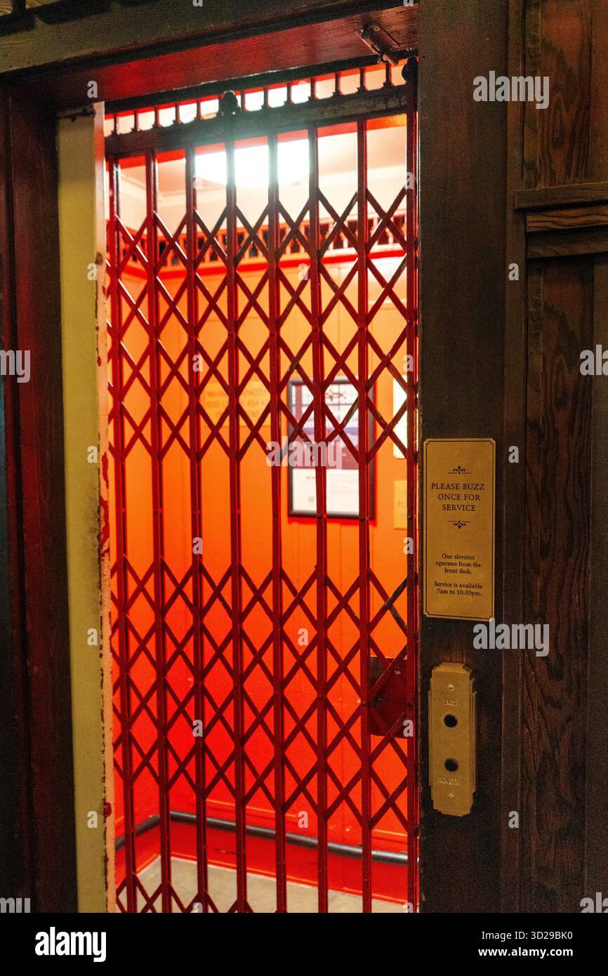 A vintage elevator with a red scissor gate and 'buzz for service' sign ...
