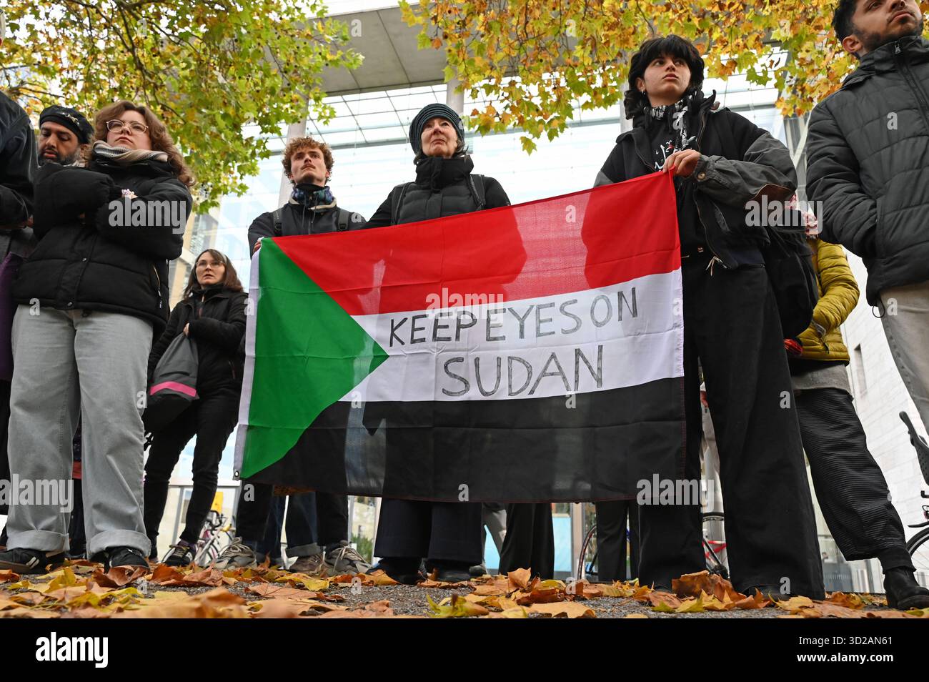 31 October 2025, Berlin: Participants hold a Sudanese flag with the inscription "Keep Eyes on ...