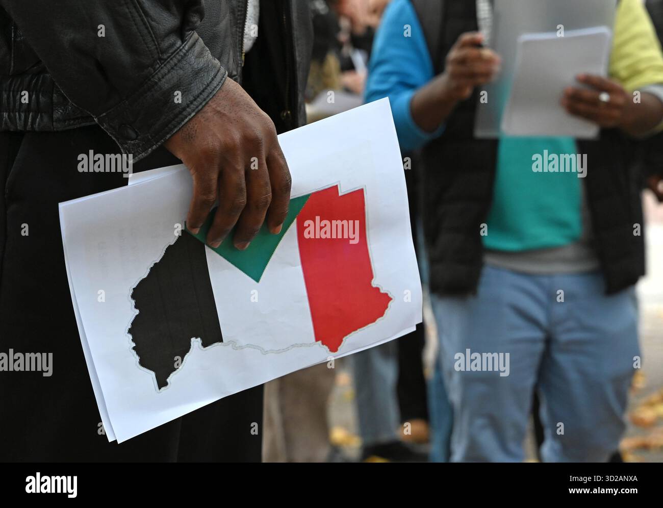 31 October 2025, Berlin: A person holds a flyer with the Sudanese flag ...
